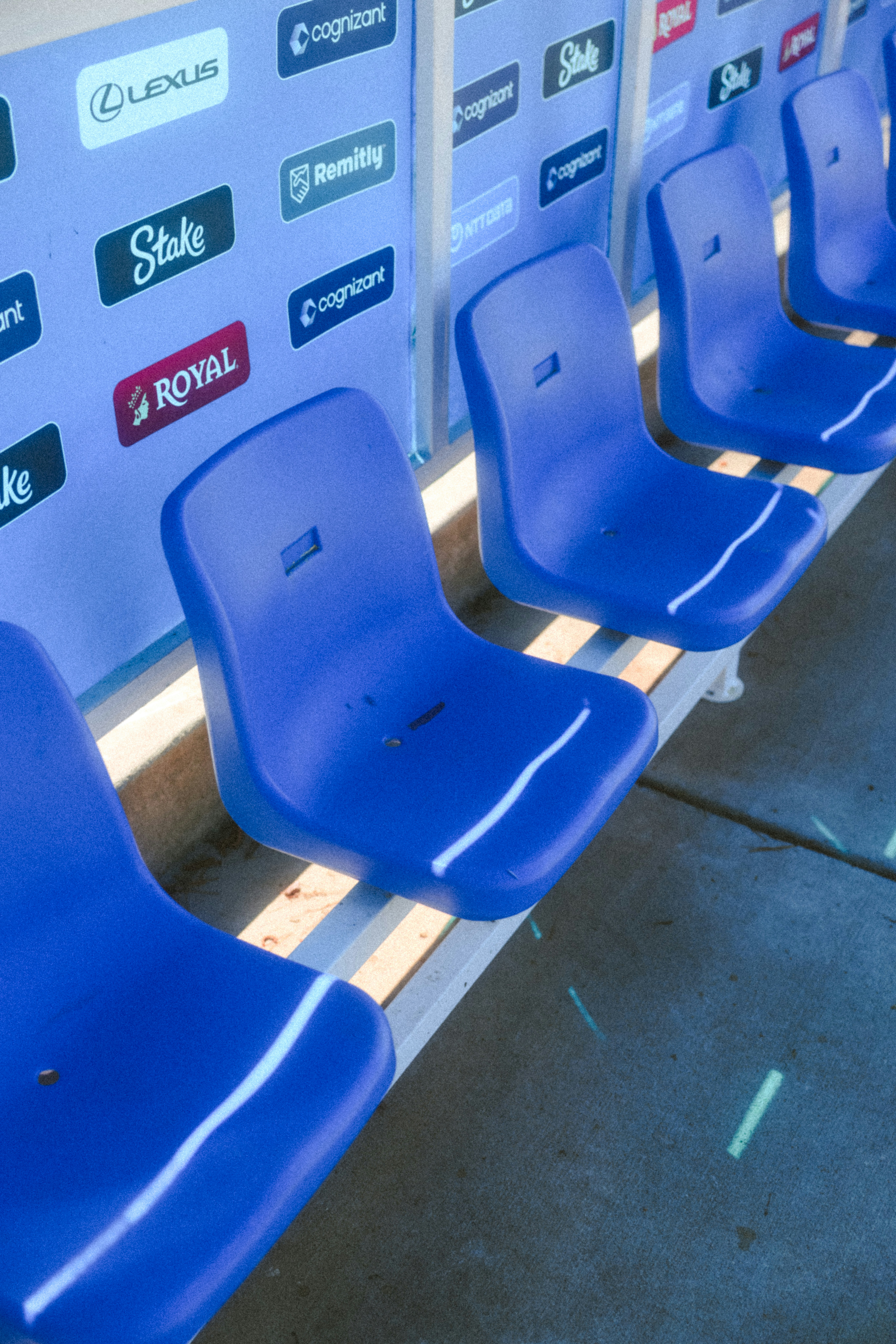 Cerulean Row: Quiet Stadium Seats Beneath a Wall of Logos