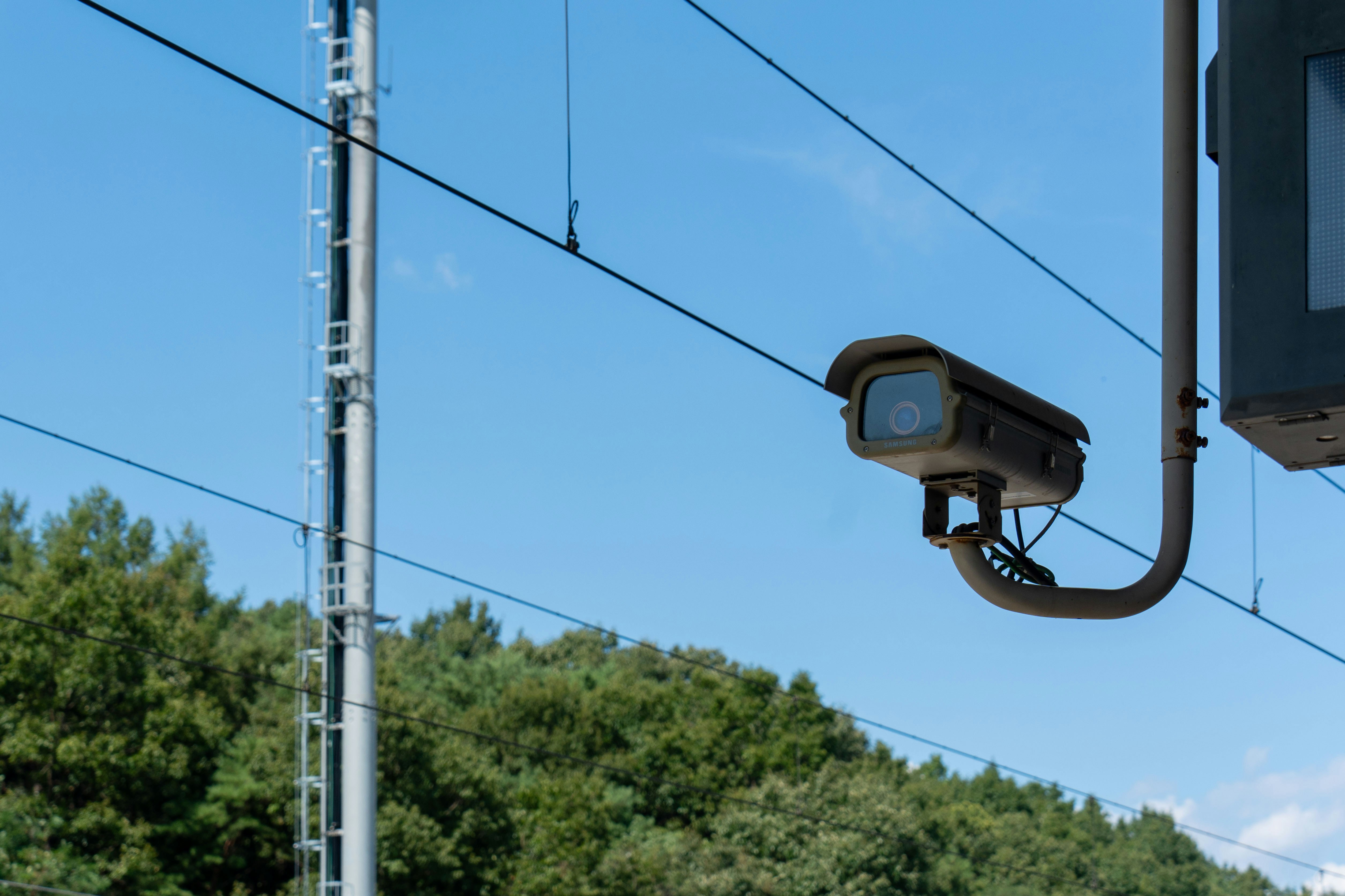Overhead Sentinel: Security camera perched above a tangle of wires under a clear blue sky