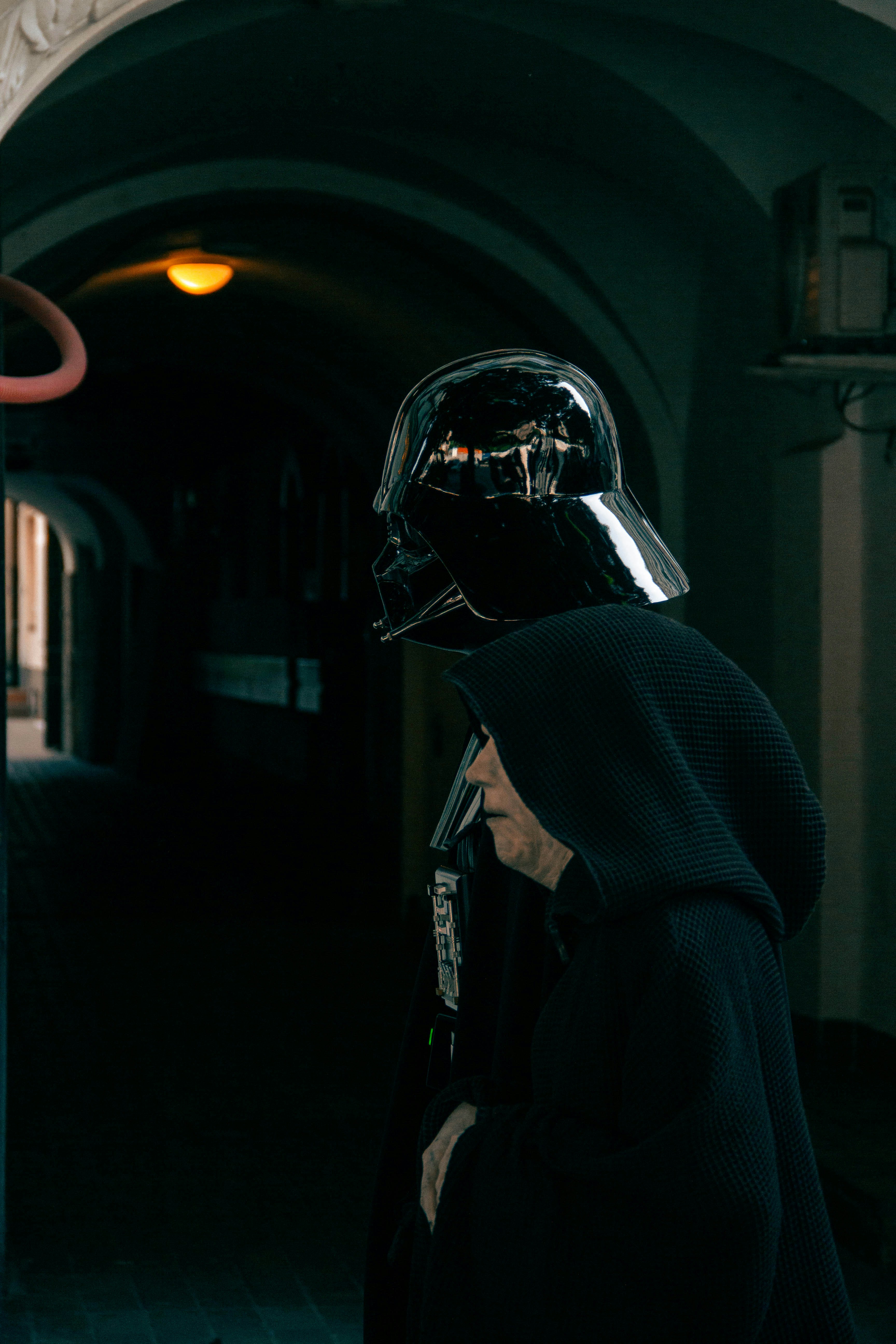 Darth vader walks through a dark, arched passage.