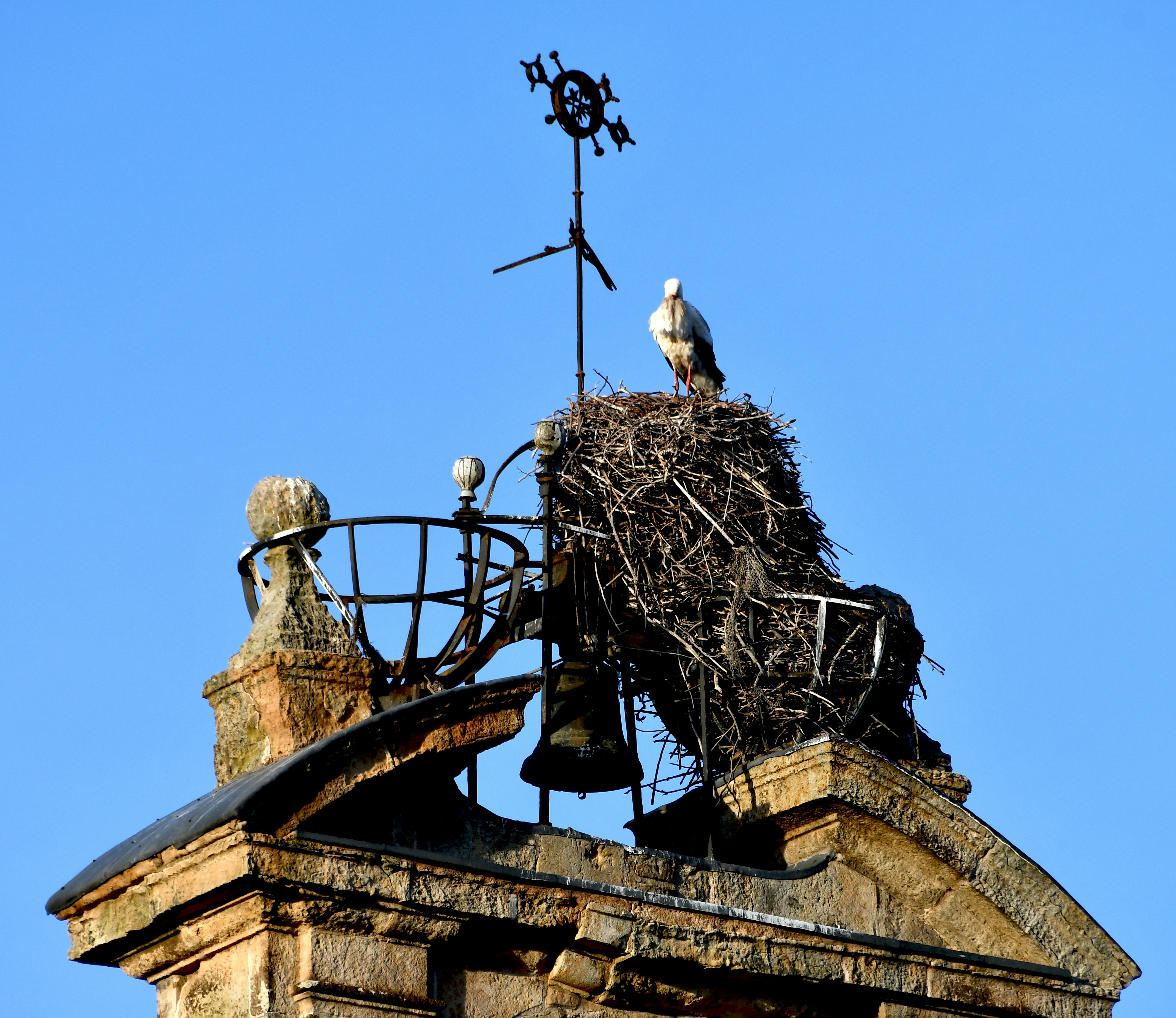 Stork Sentinel: Nest Crowned atop a Weathered Roof Against a Bright Blue Sky