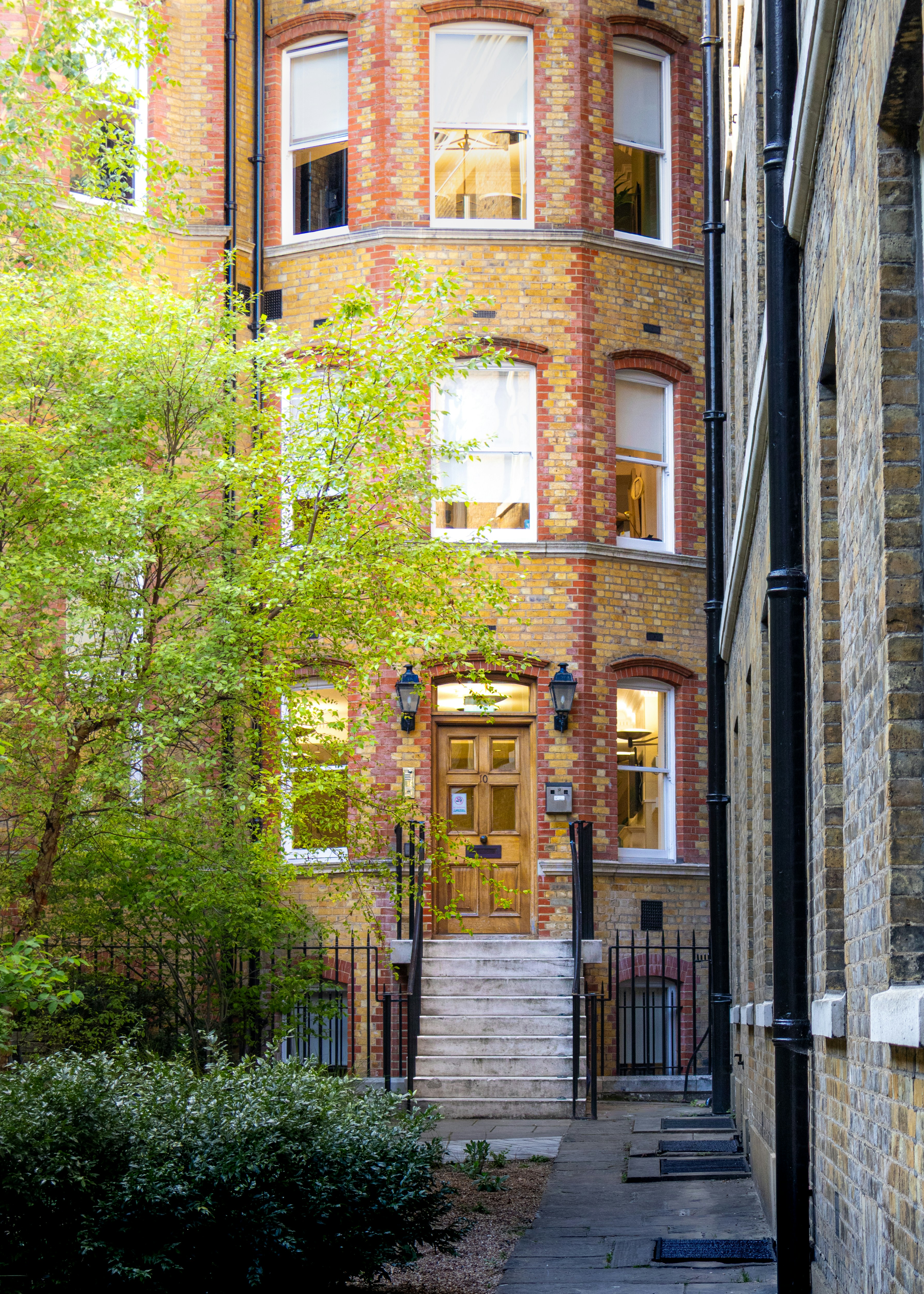 Charming brick building framed by lush greenery, showcasing an inviting entrance with stairs and decorative lamps.