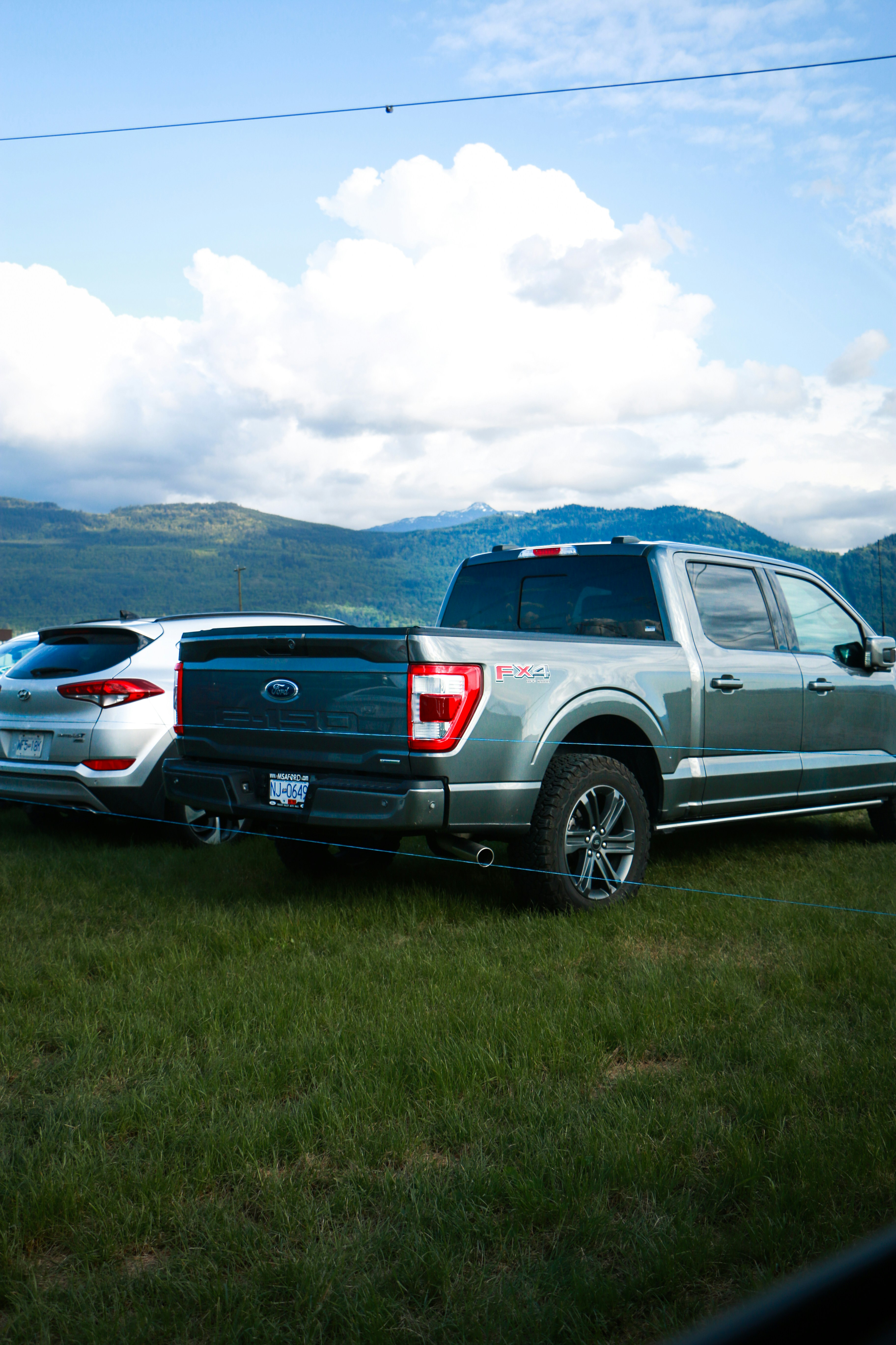 Front-Row Fieldscape: A Silver Pickup Anchors the Grass Under Alpine Skies