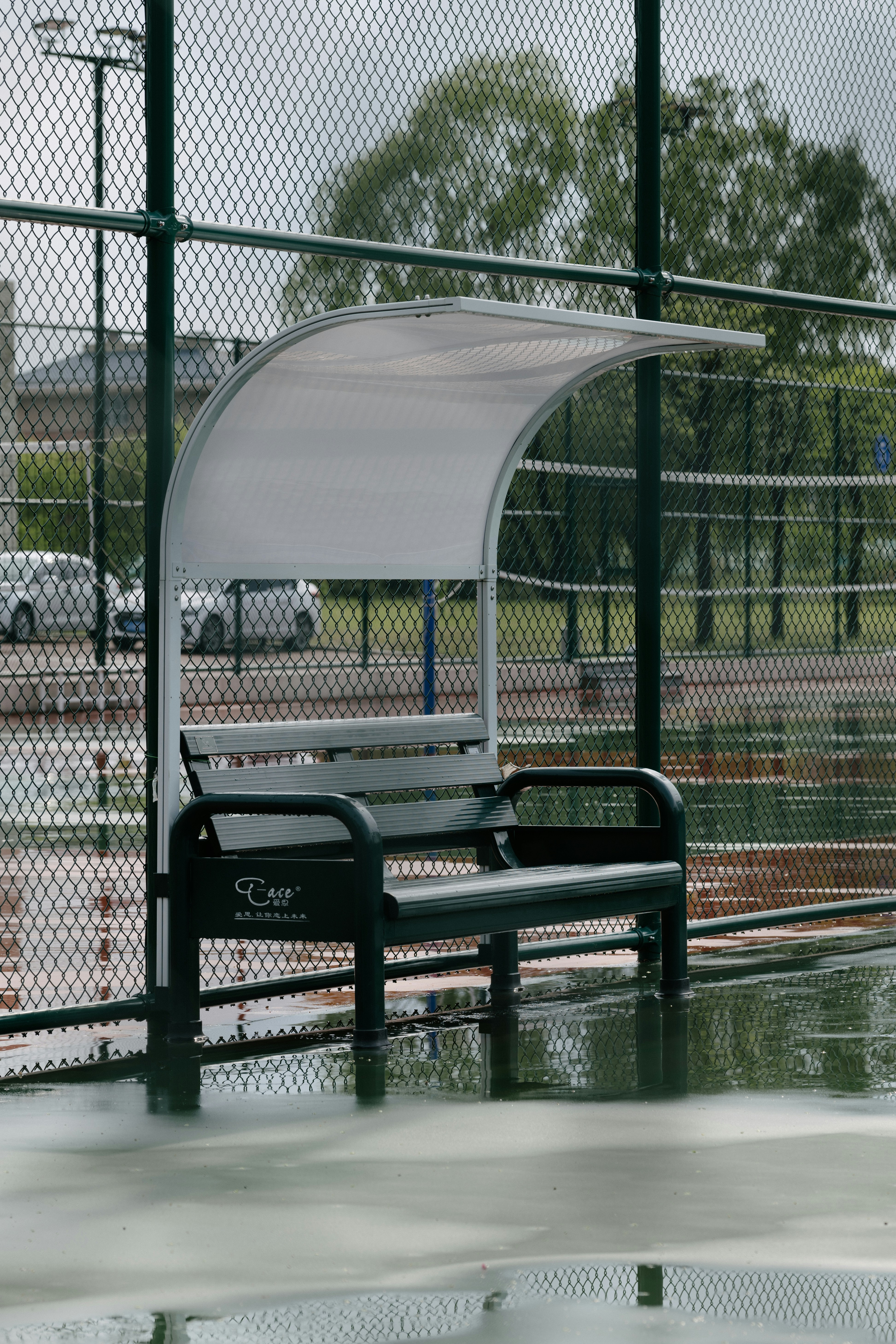 Curved Shelter, Rain-Kissed Bench Behind a Chain-Link Fence