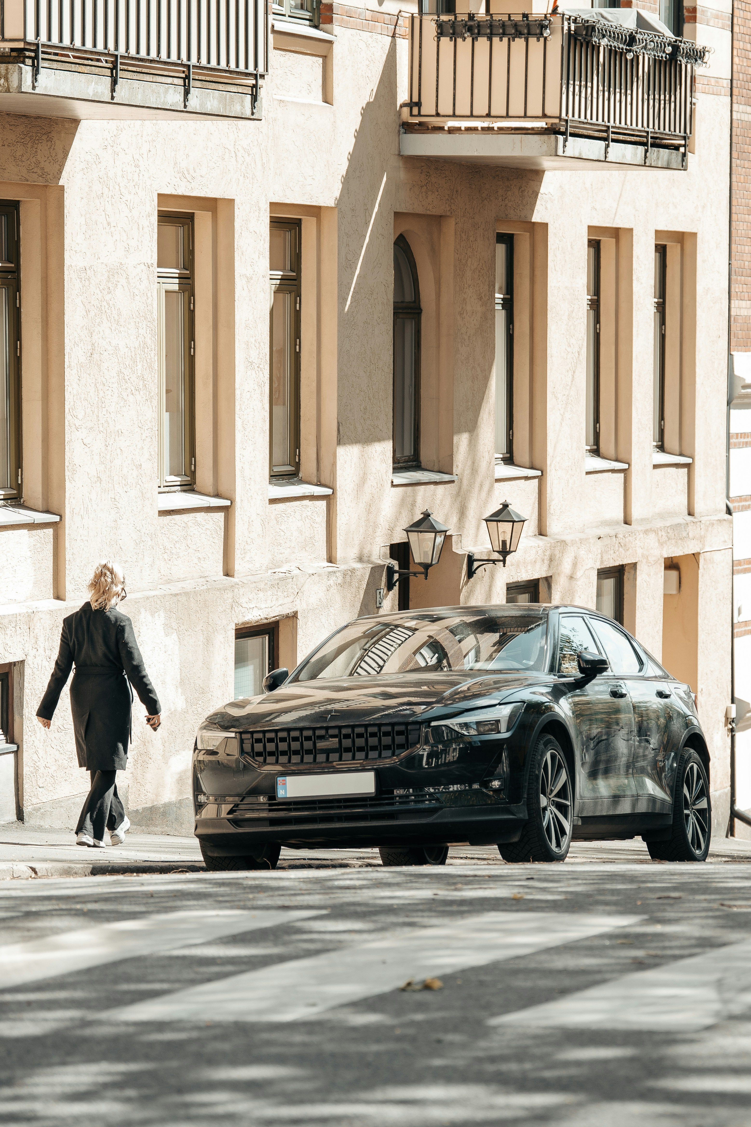 Sunlit Street Noir: A Black SUV by Warm Facades as a Pedestrian Passes