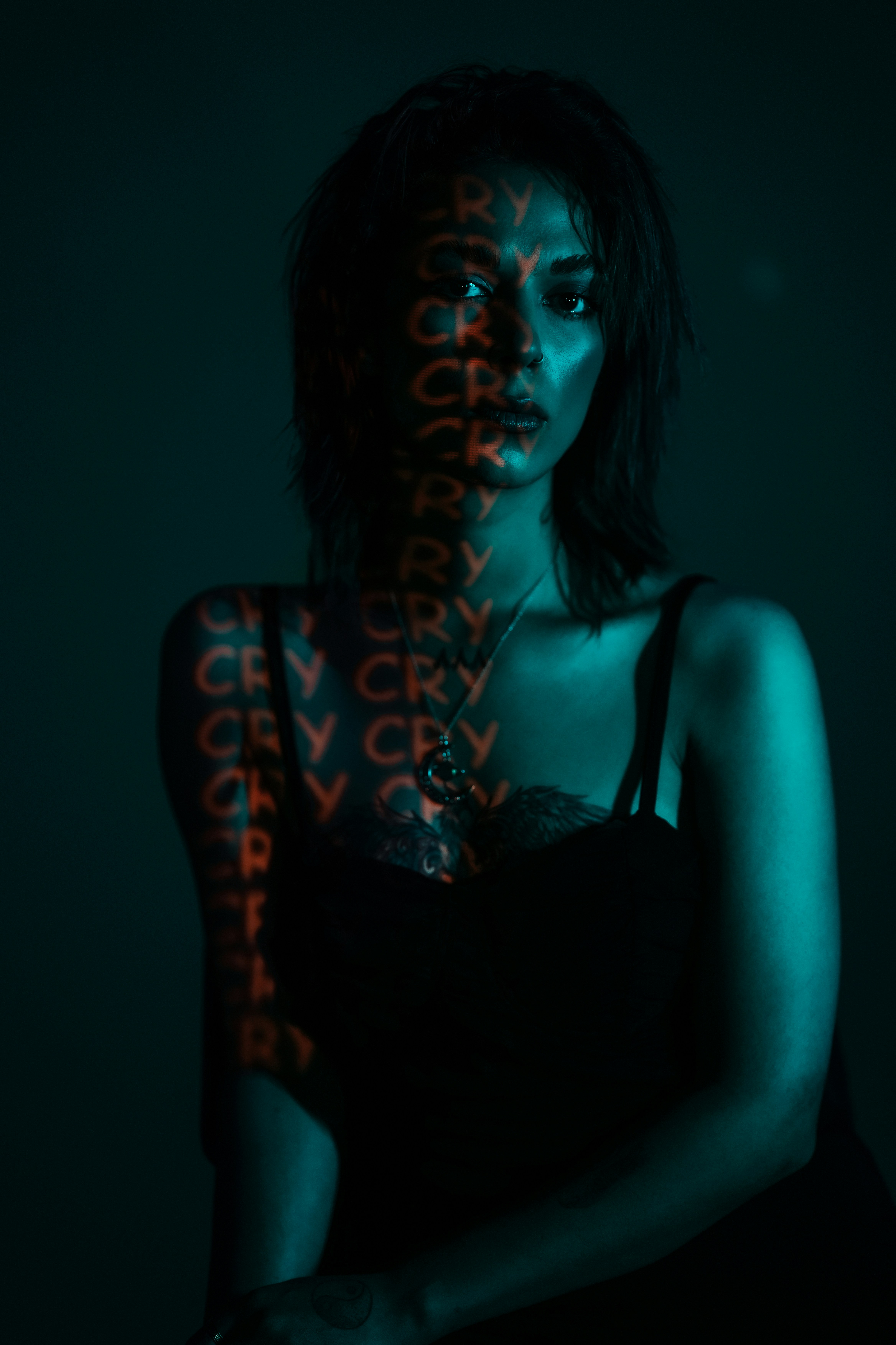 A figure illuminated in moody lighting, with the word 'CRY' projected across their face and body, creating a striking visual narrative.