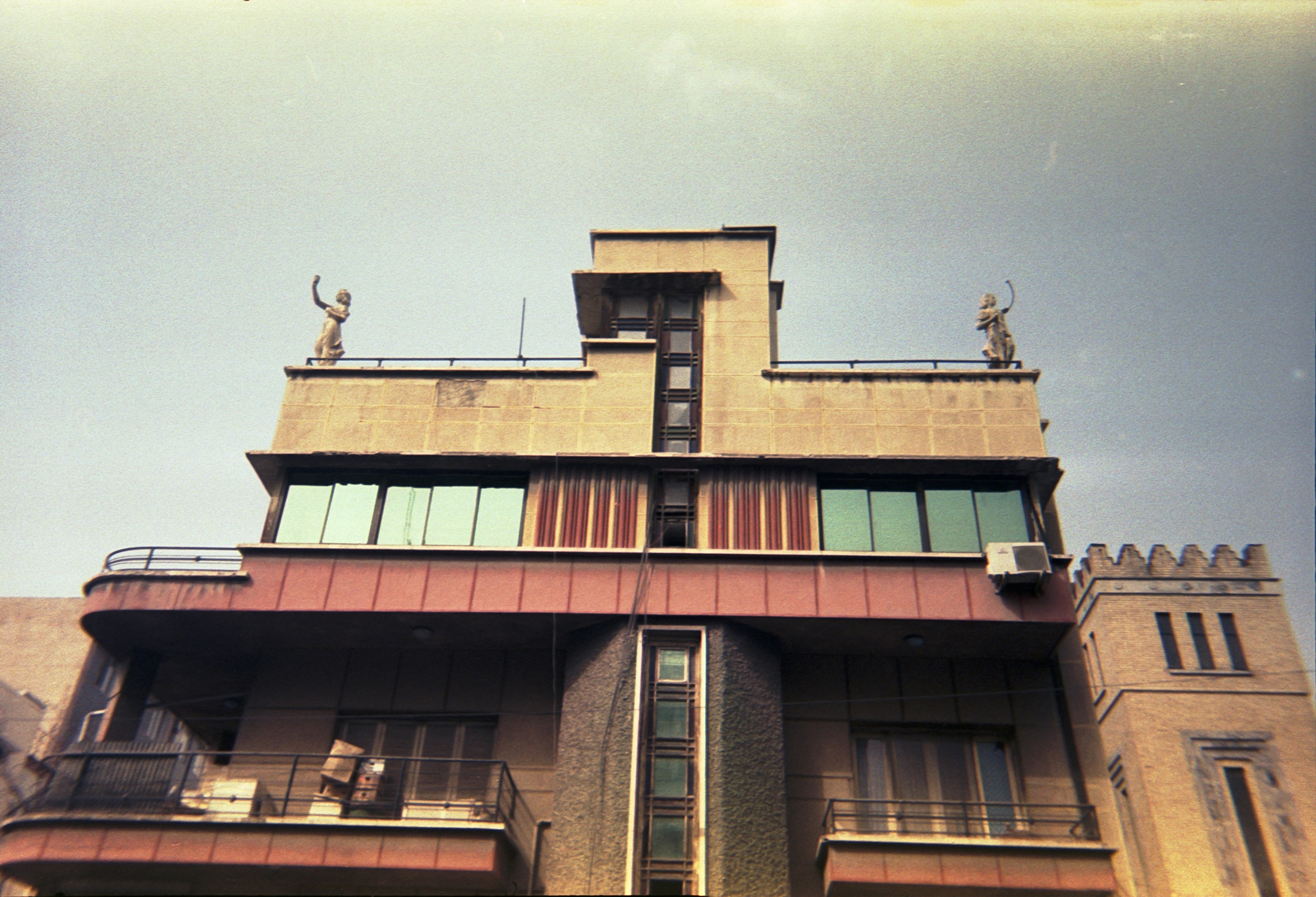 Sunlit Tiers: A Balcony-Layered Facade Crowned by Statues on a Retro Tower