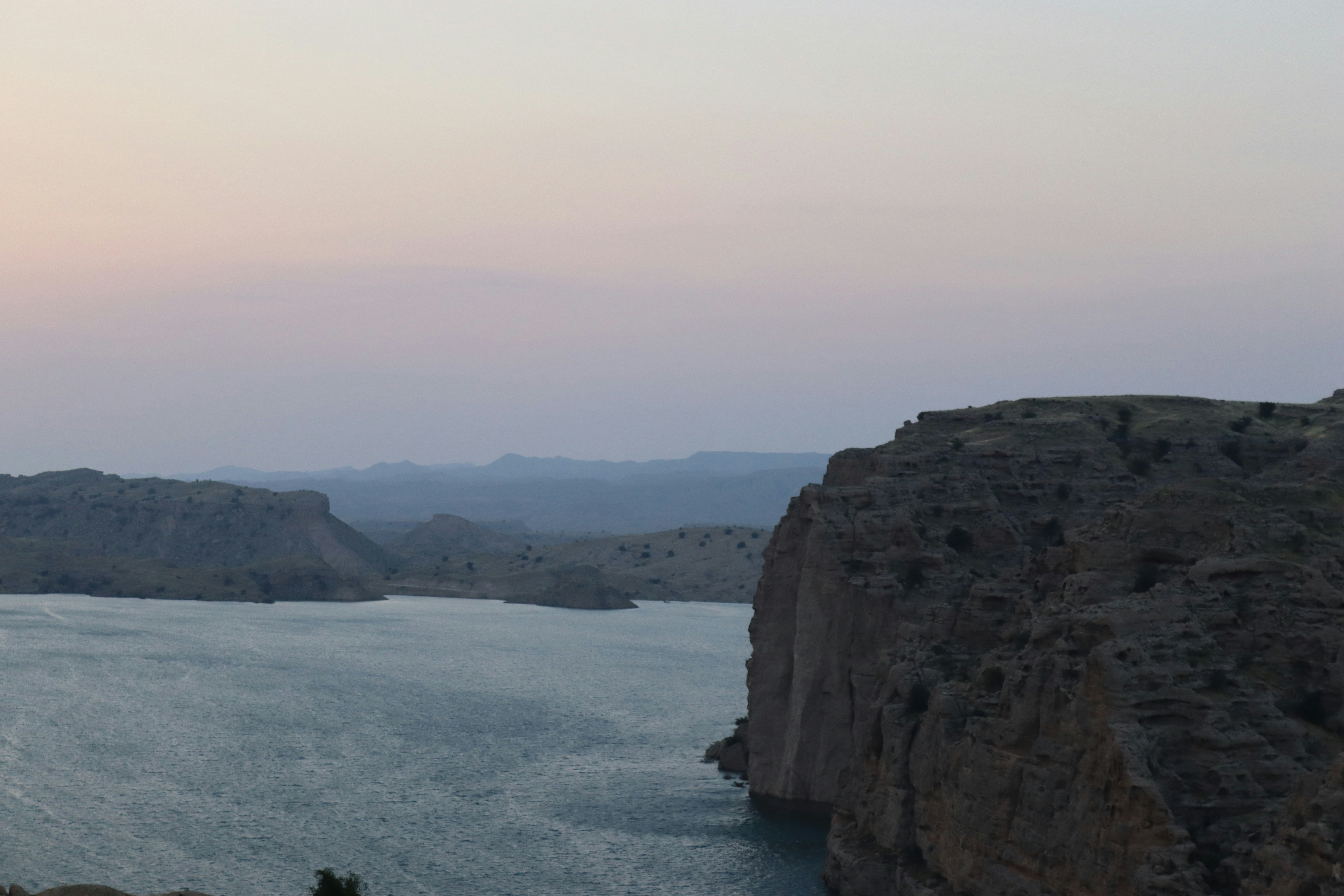 Gentle curves of a canyon meet the tranquil waters under a pastel sky at twilight.