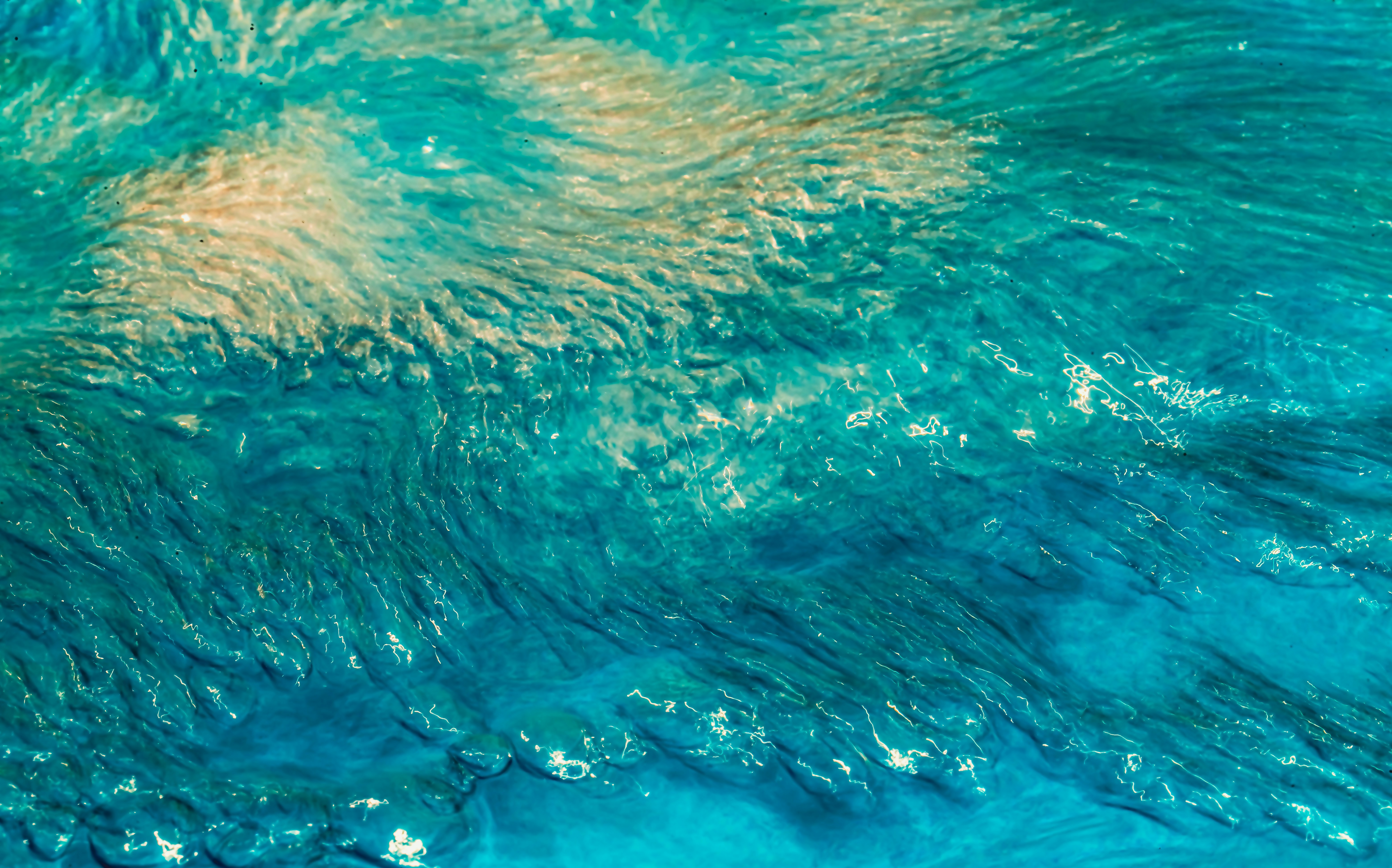 Vibrant turquoise water swirls with dynamic movement, capturing the essence of a lively aquatic scene. The interplay of light and shadow enhances the fluidity of the waves.