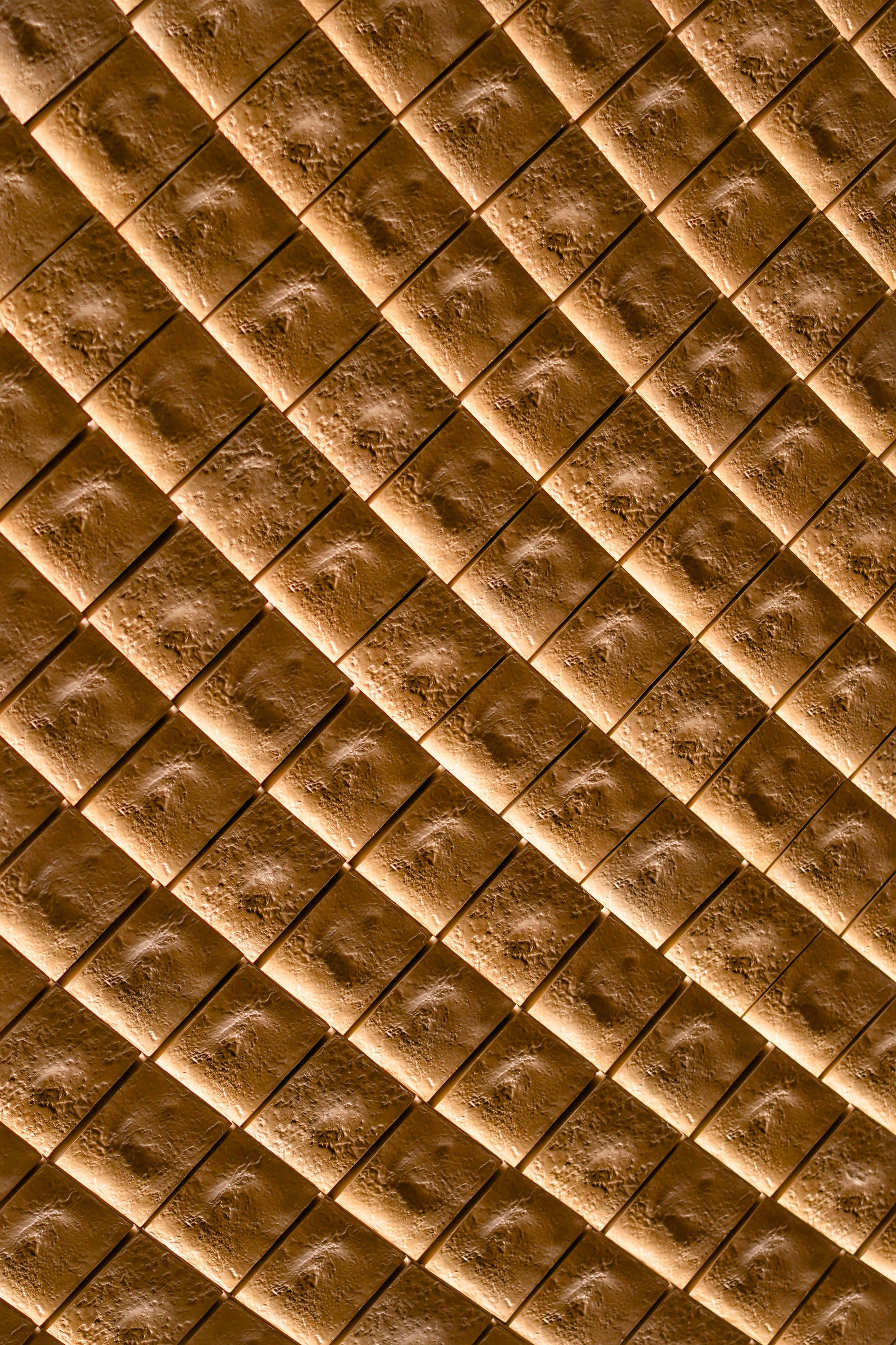 Textured surface of interlocking tiles arranged in a diagonal pattern, showcasing intricate details and warm tones.