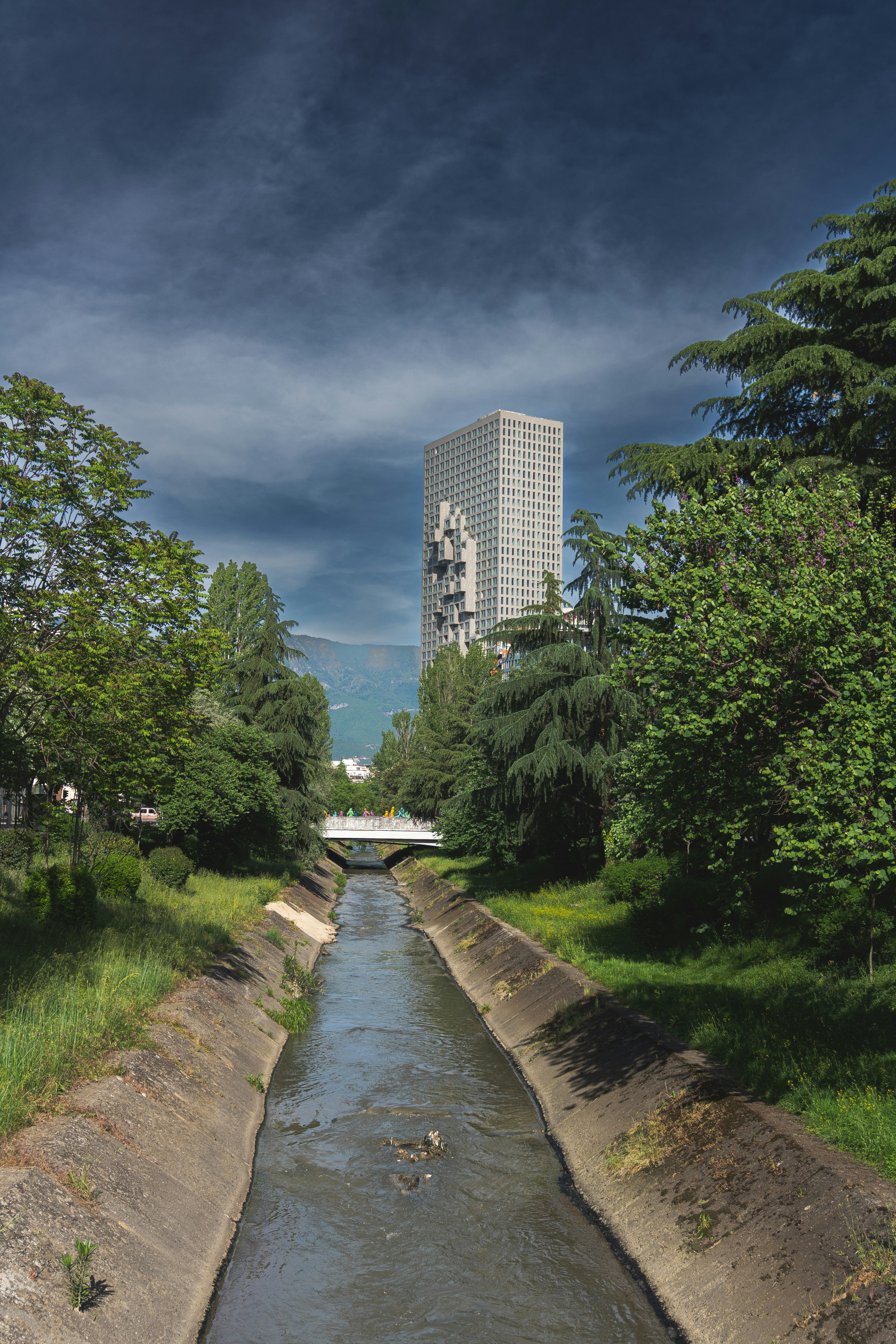 Canal Corridor, Glassy Skyline: Framing a Geometric High-Rise Through Green Canopies