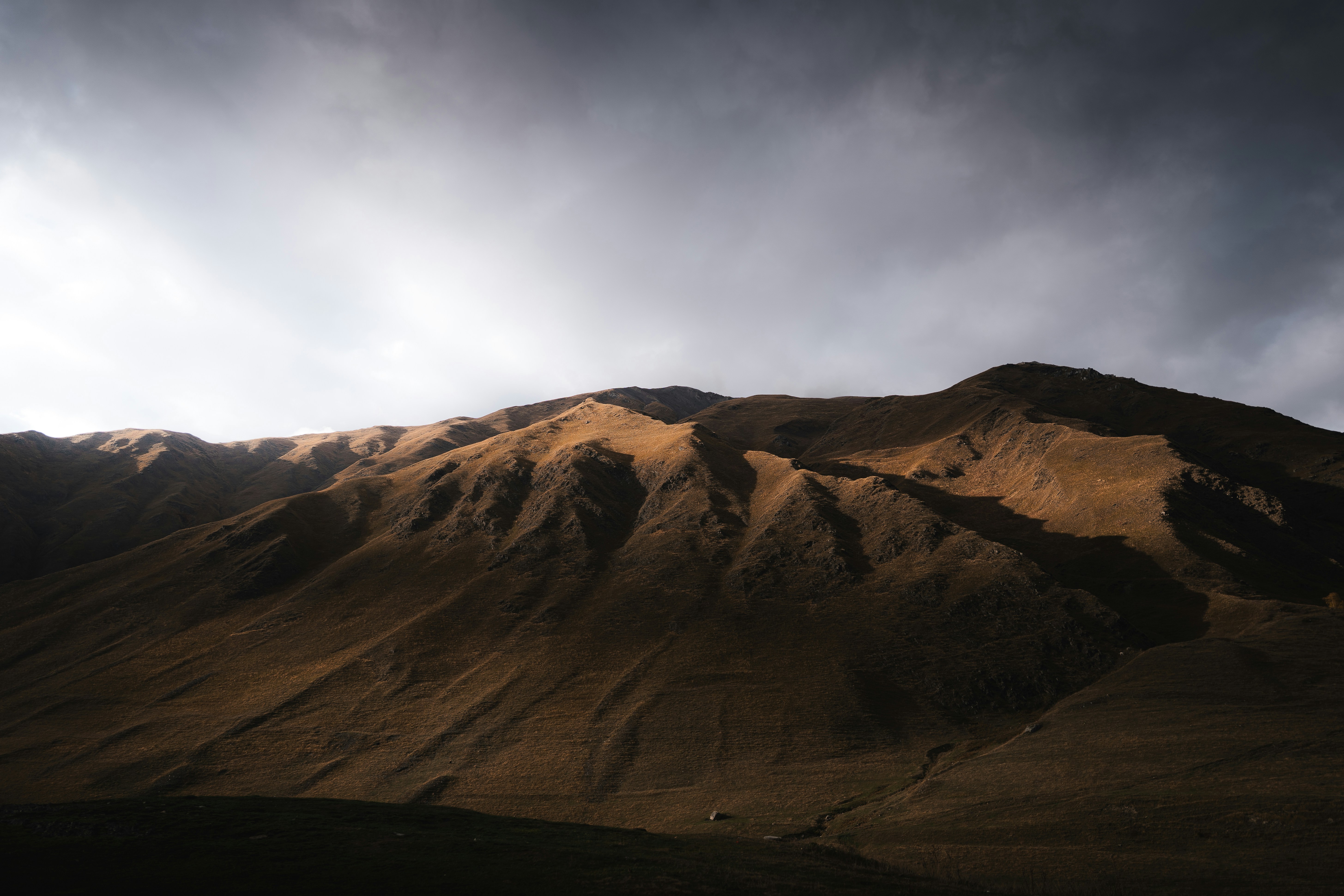 Dramatic mountain landscape bathed in warm sunlight against a moody sky. The rugged terrain showcases the interplay of light and shadow.