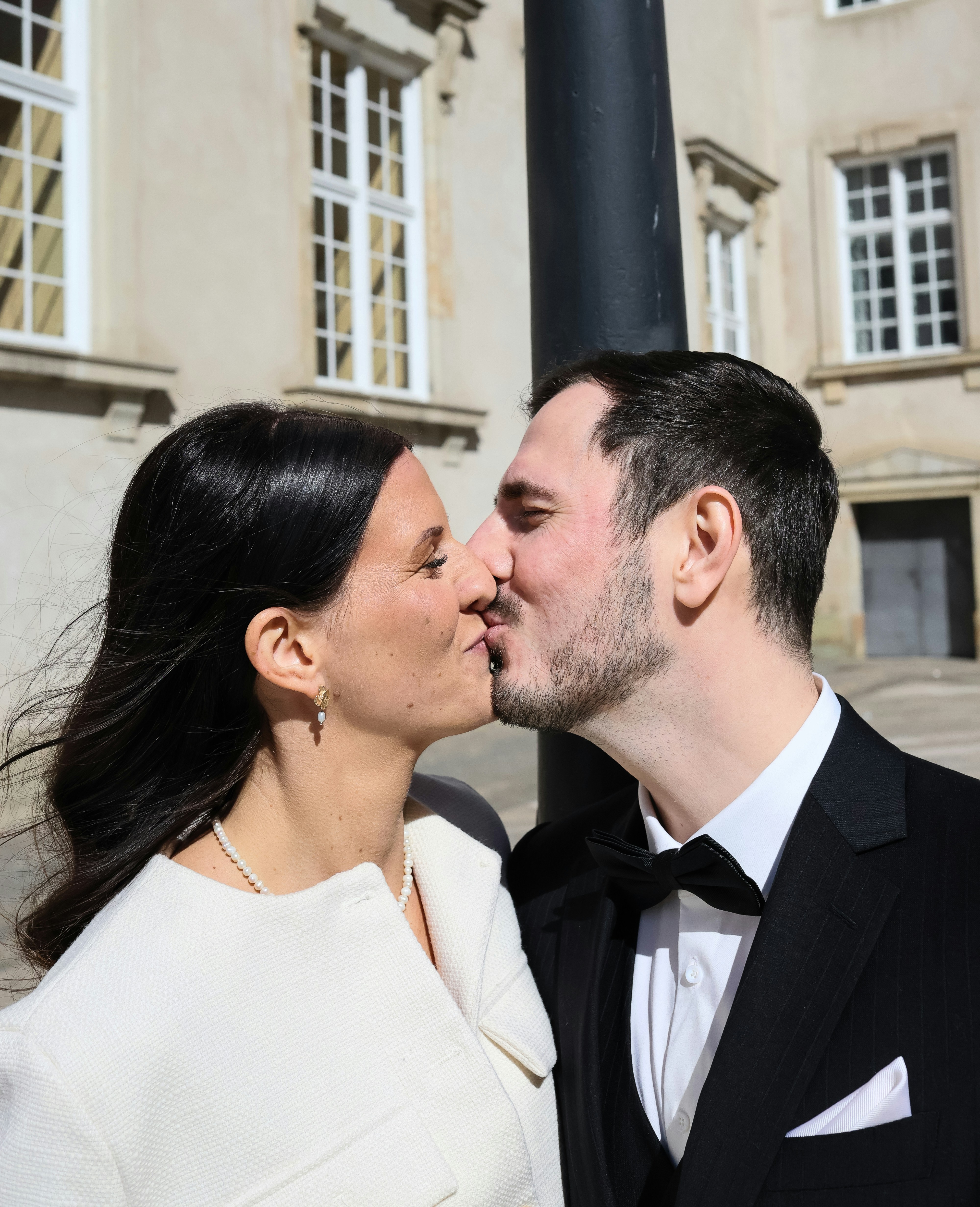 Sunlit Courtyard Kiss: Bride and Groom in Sharp Focus Amid Historic Facade