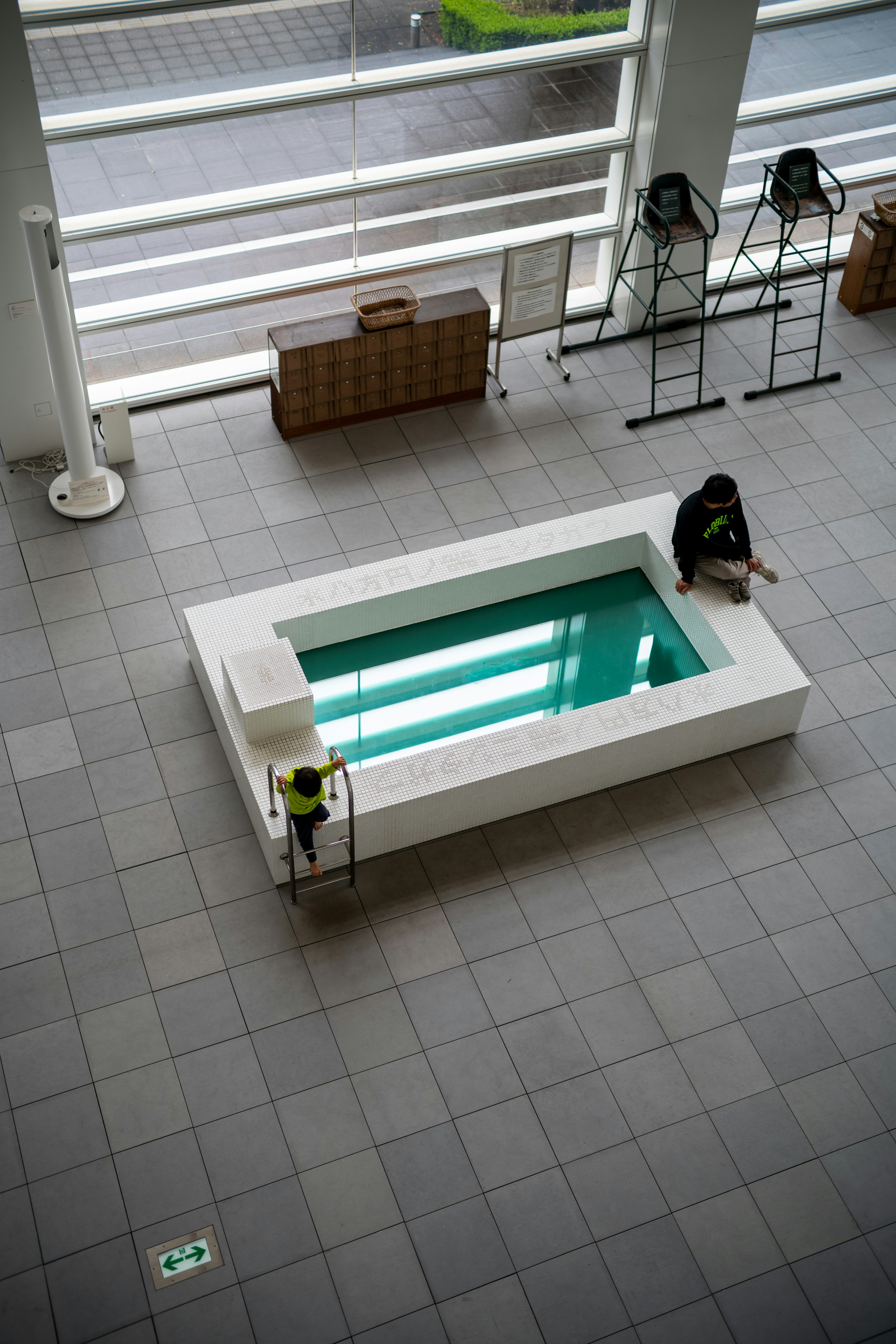 Two individuals engaging with a minimalist water feature in a contemporary space, showcasing the interplay of design and reflection.