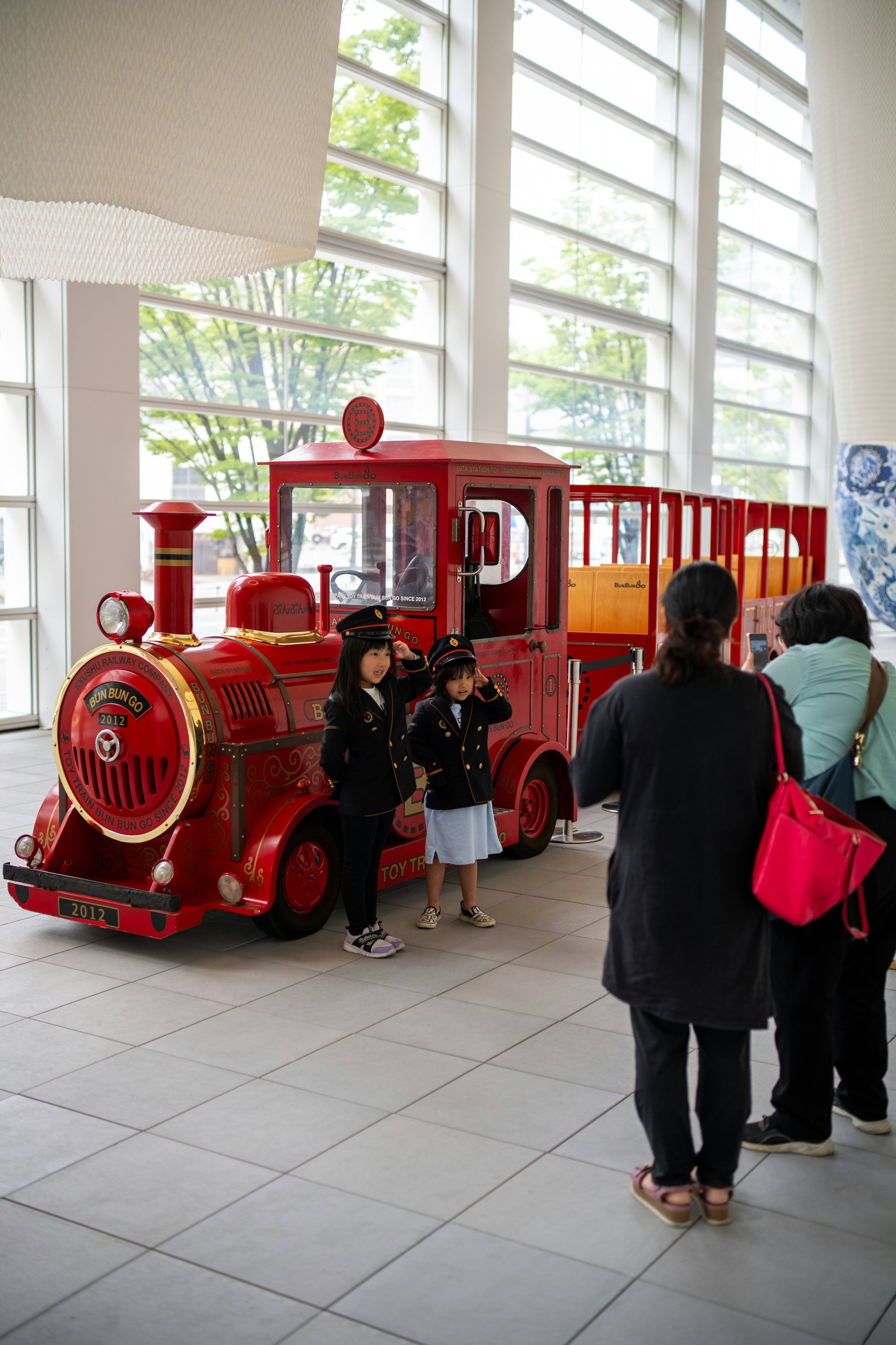 Tiny conductors in a grand showroom: red locomotive and curious children