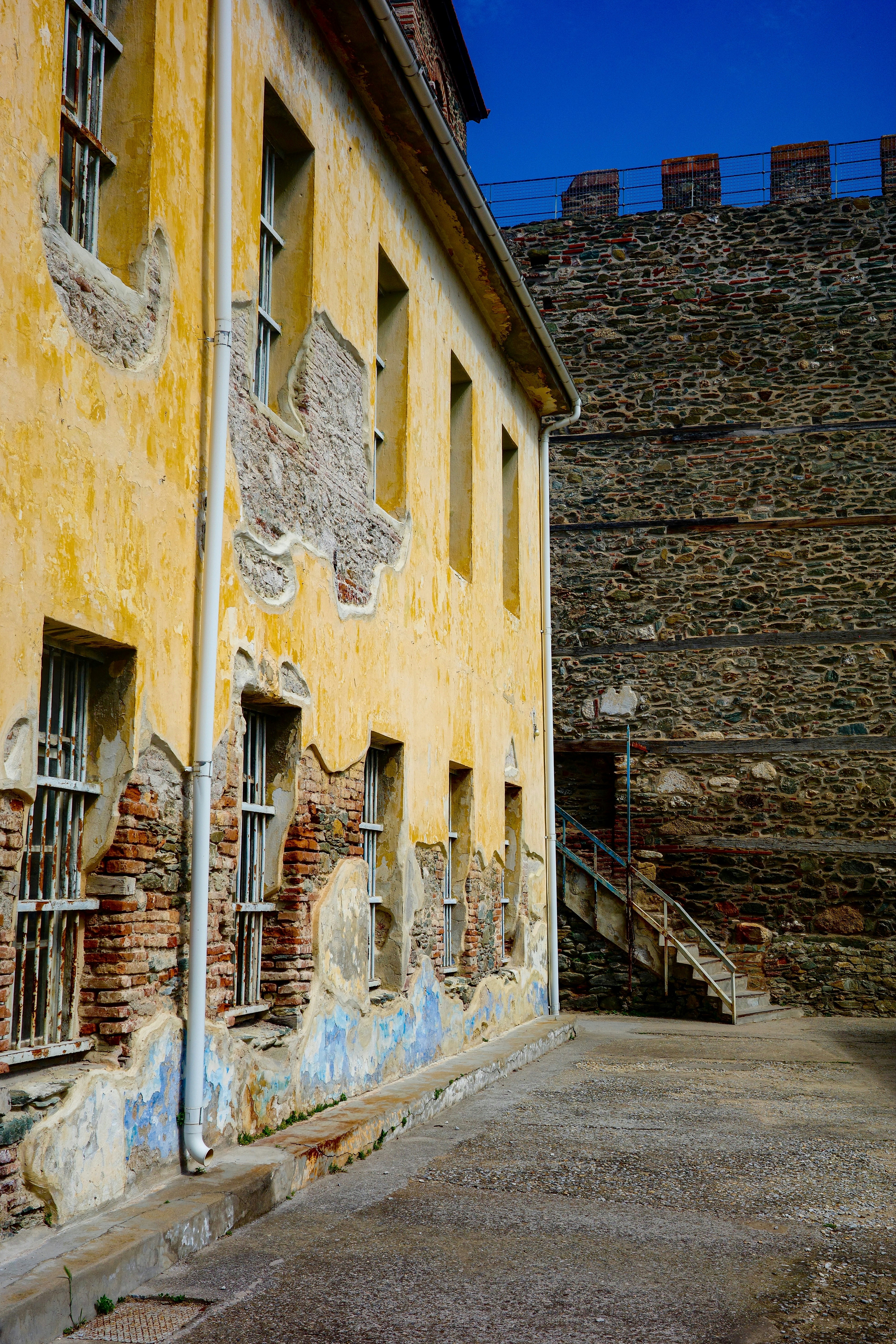 Sunlit Facade and Stone Ramp: A Textured Corridor Between Yellow Walls and Ancient Masonry