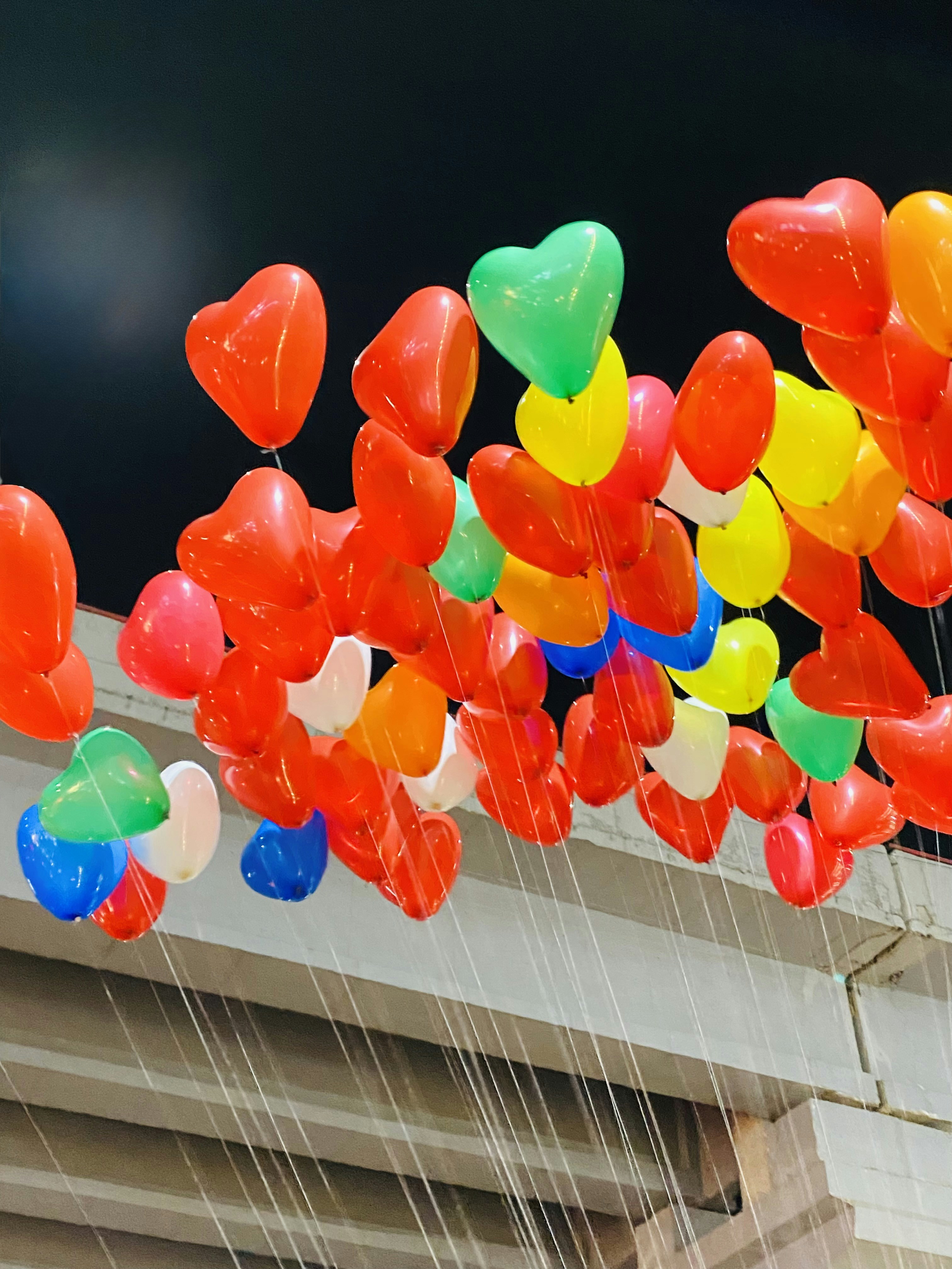Heart-shaped balloons of many colors float together.