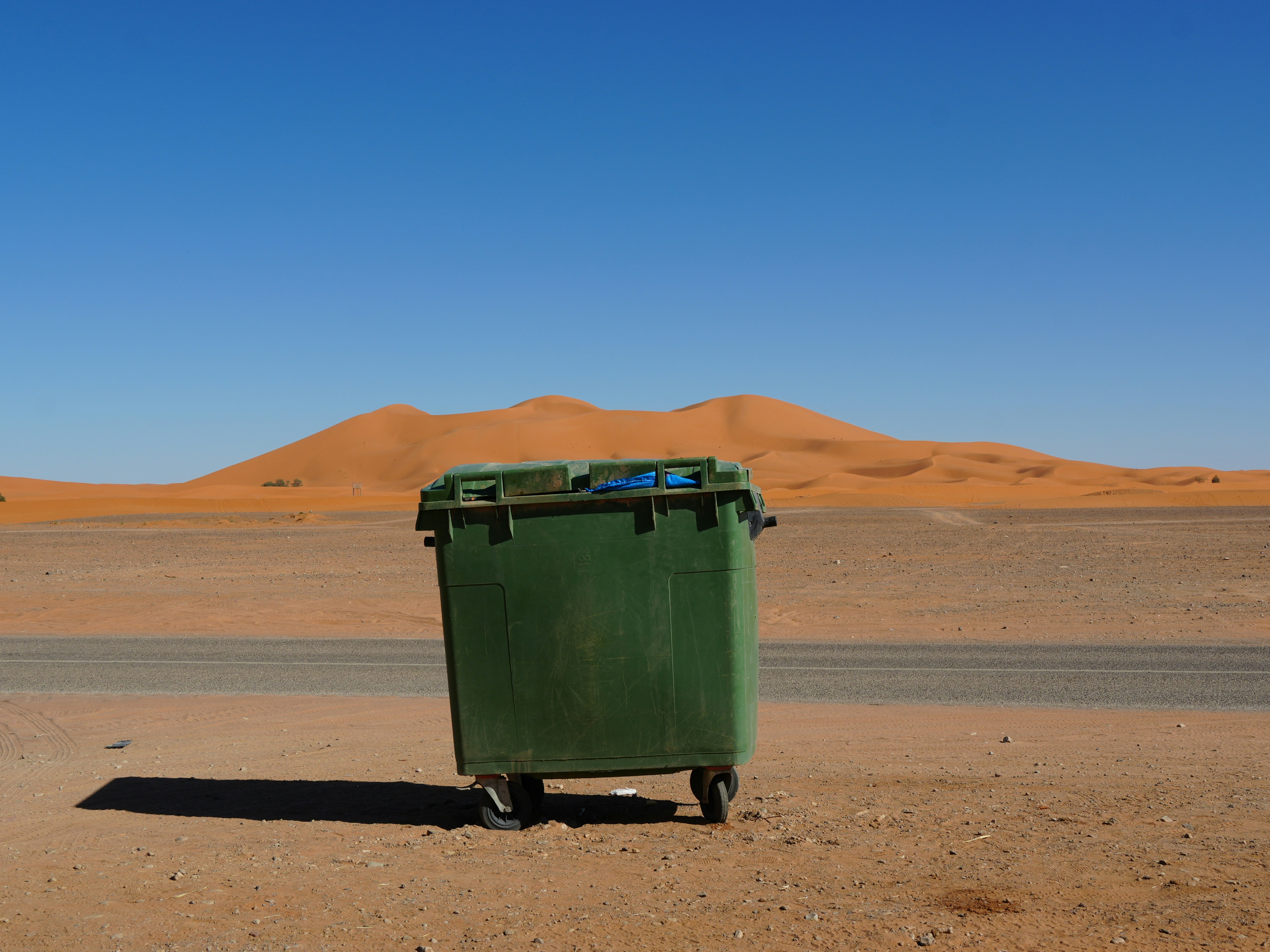 A green trash bin sits in the desert.