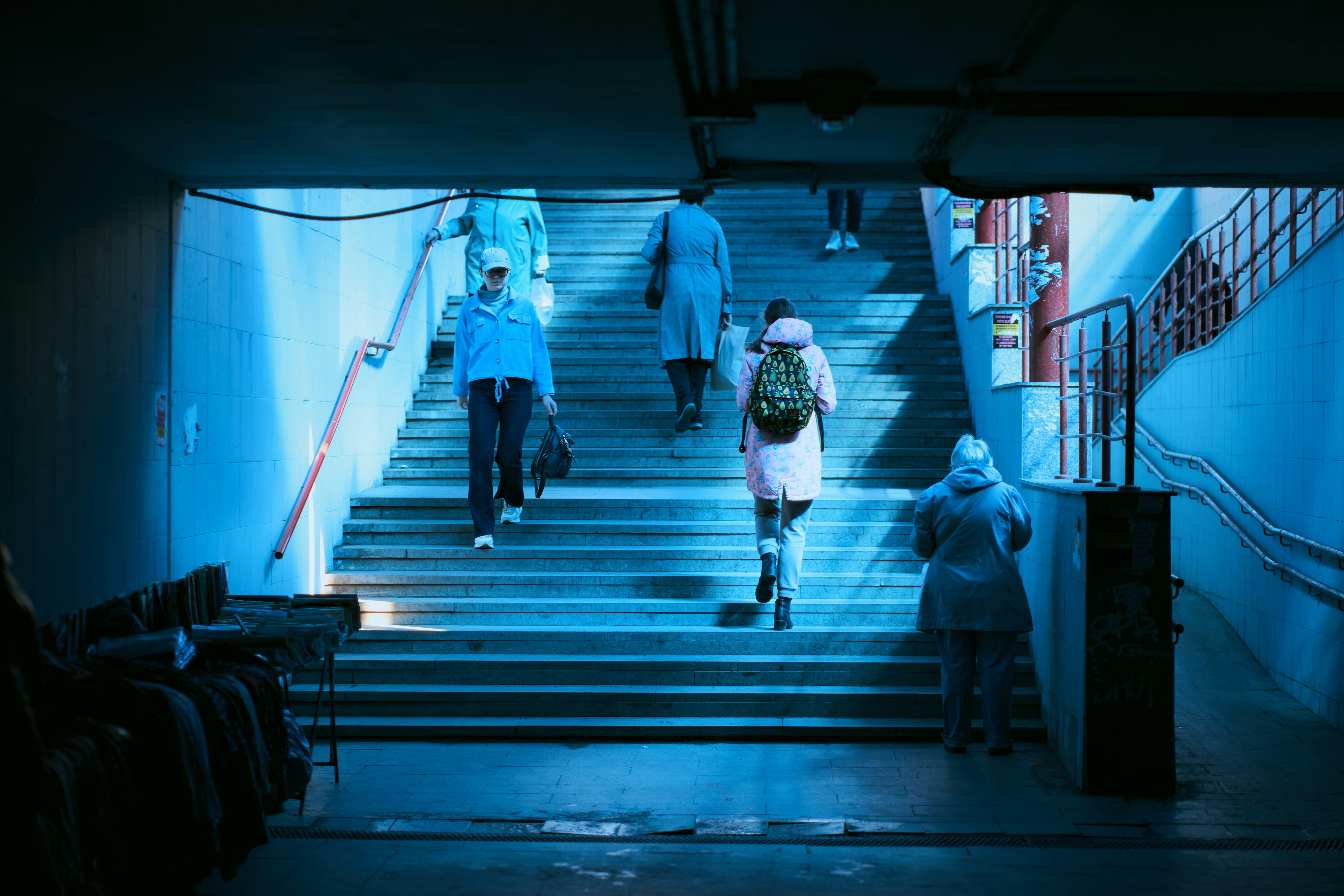 Cyan Stairwell Chronicles: Pedestrians Ascend Beneath Neon Blue