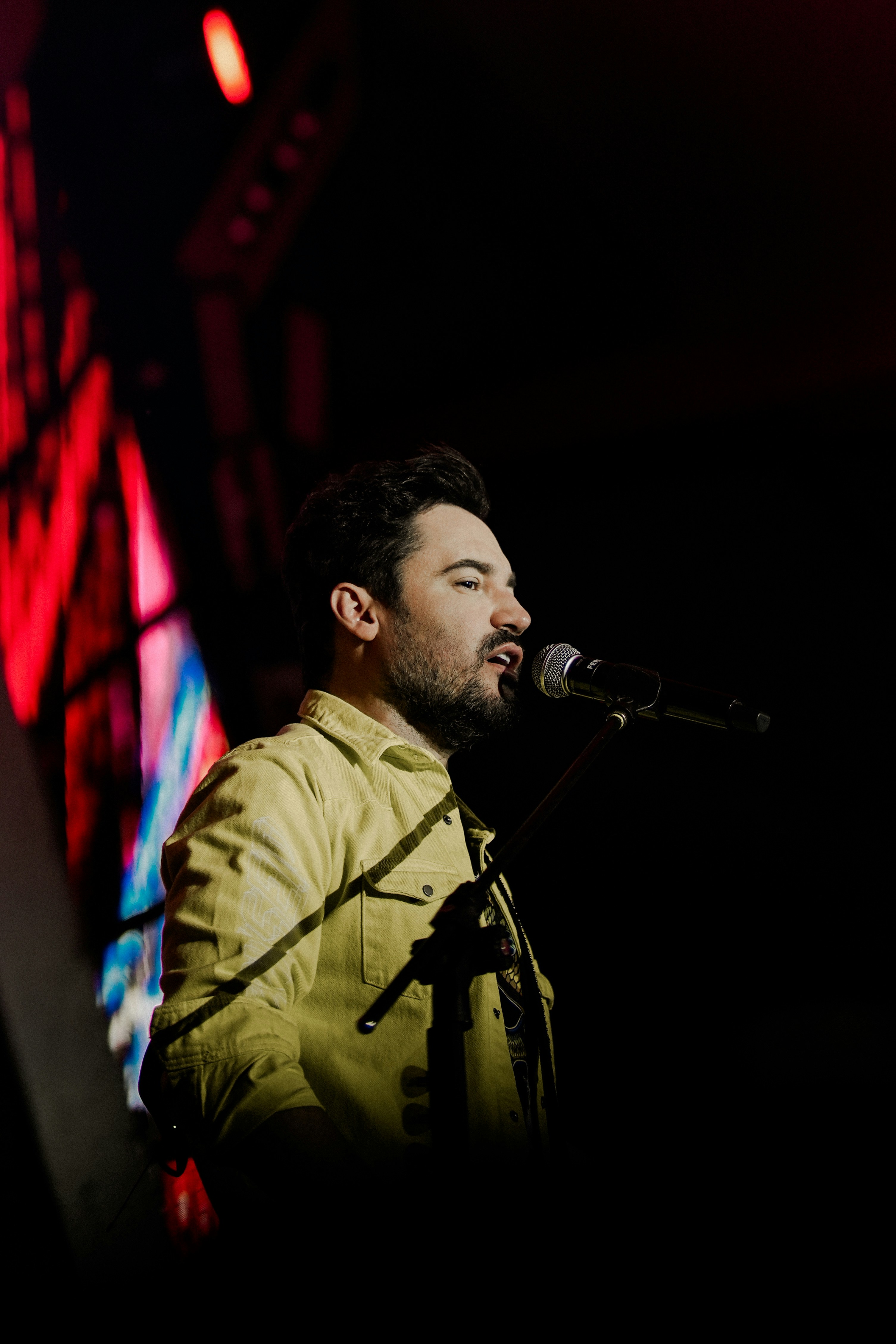 A performer passionately singing into a microphone, illuminated by vibrant stage lights, creating a dynamic atmosphere.