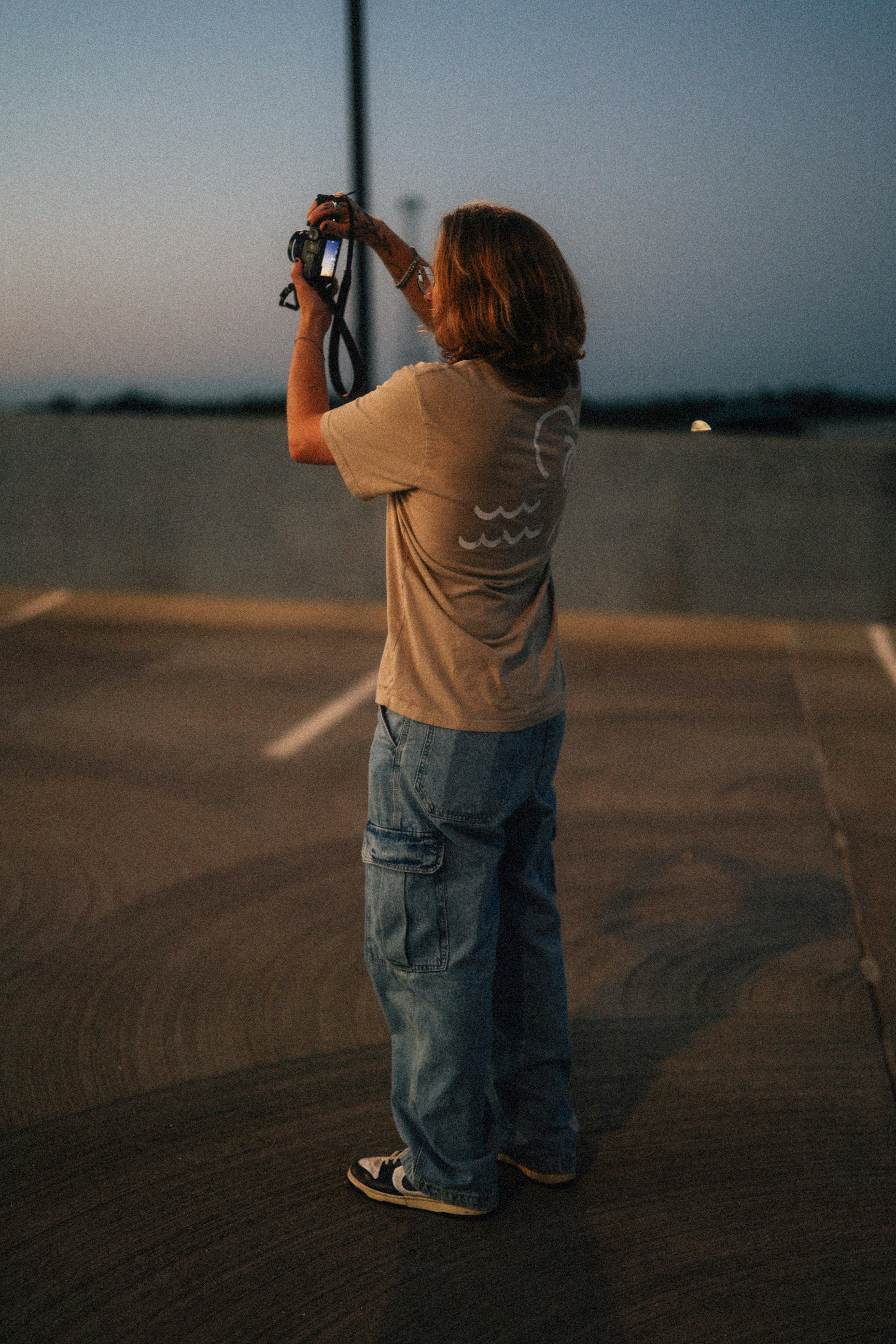 Person standing on a parking structure, holding a camera while preparing to take a photograph as twilight descends.