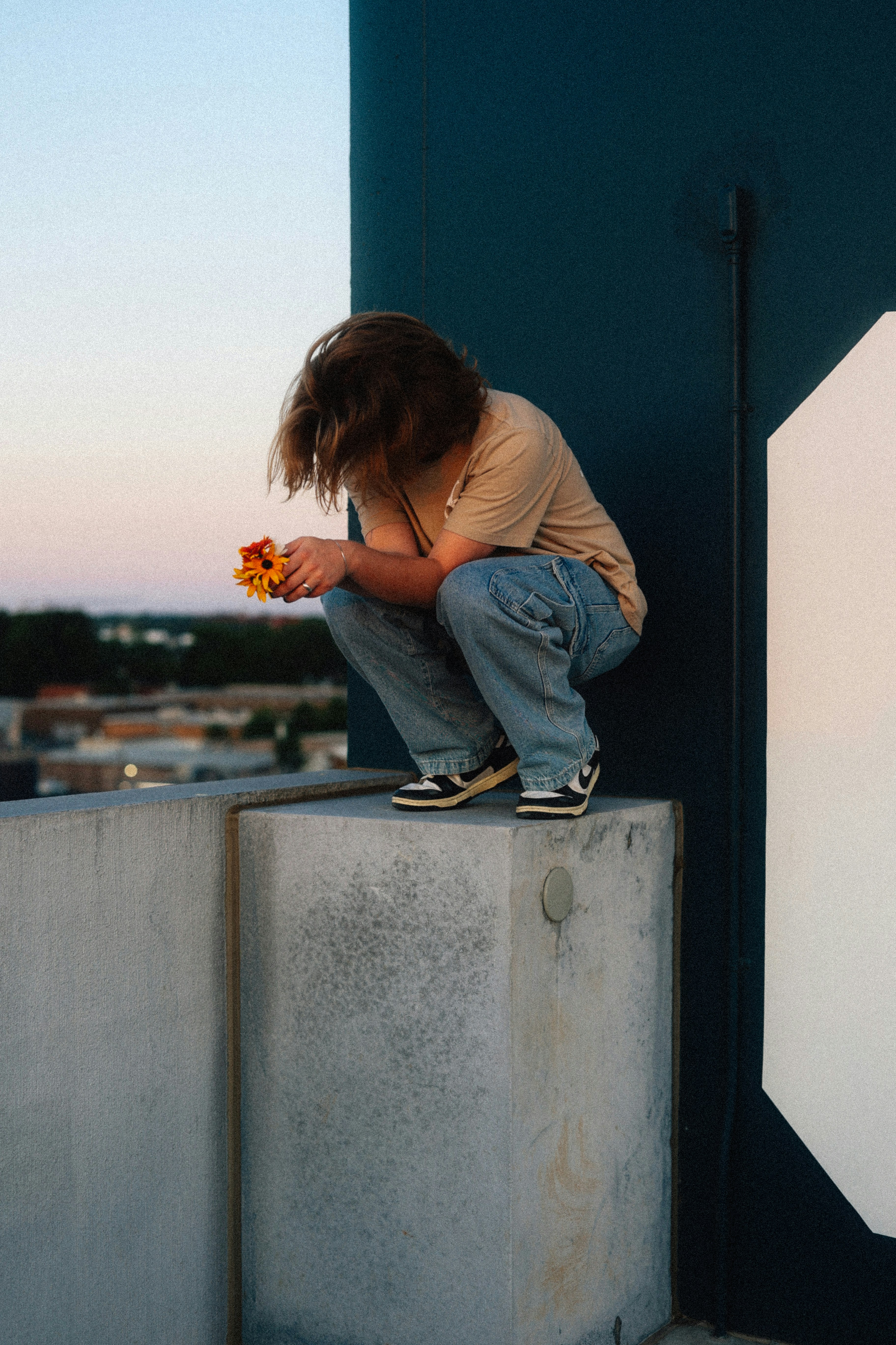 A person holds flowers while crouching on a ledge. photo – Free Image ...