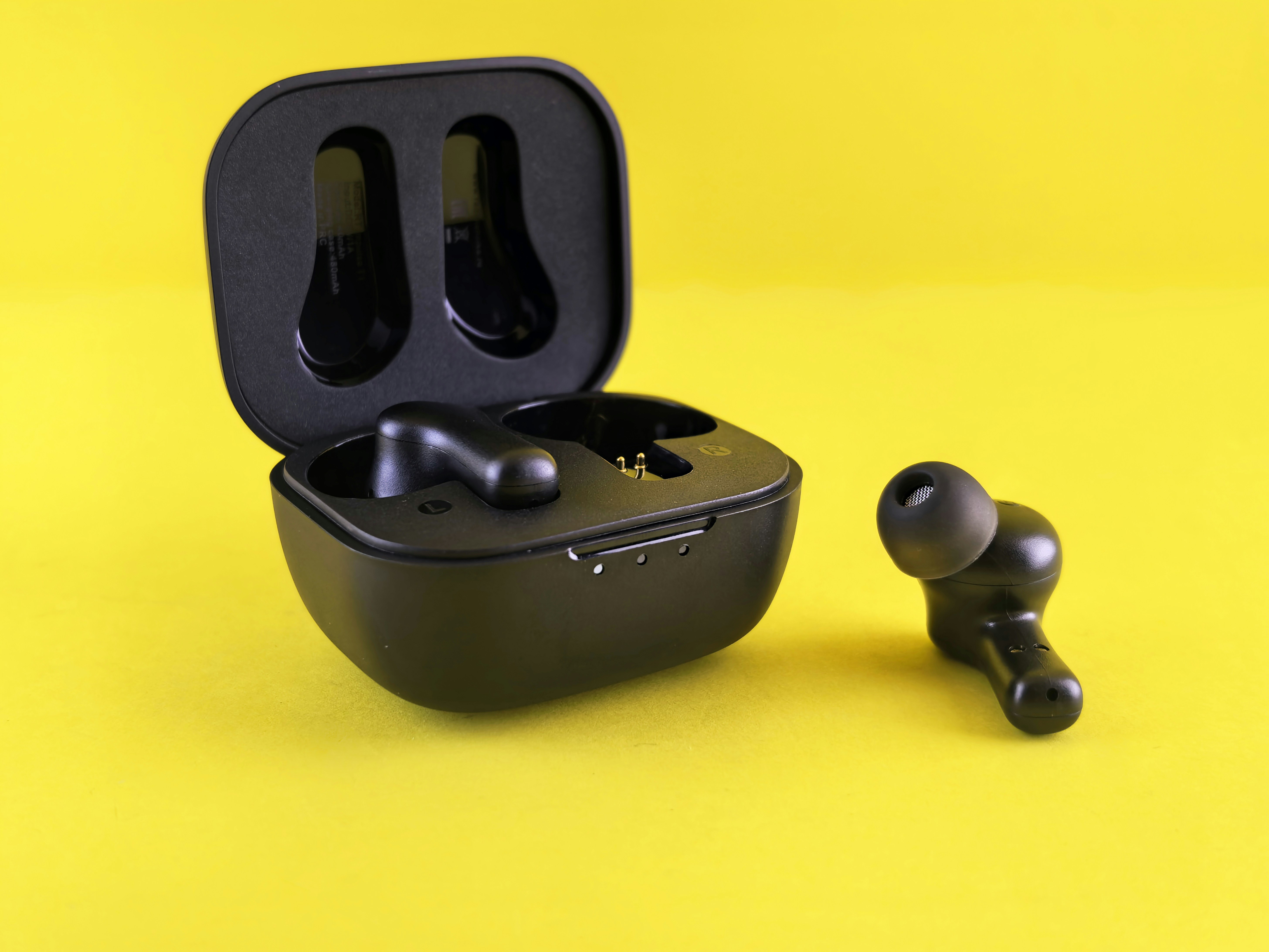 Black wireless earbuds resting beside their sleek charging case against a vibrant yellow background.