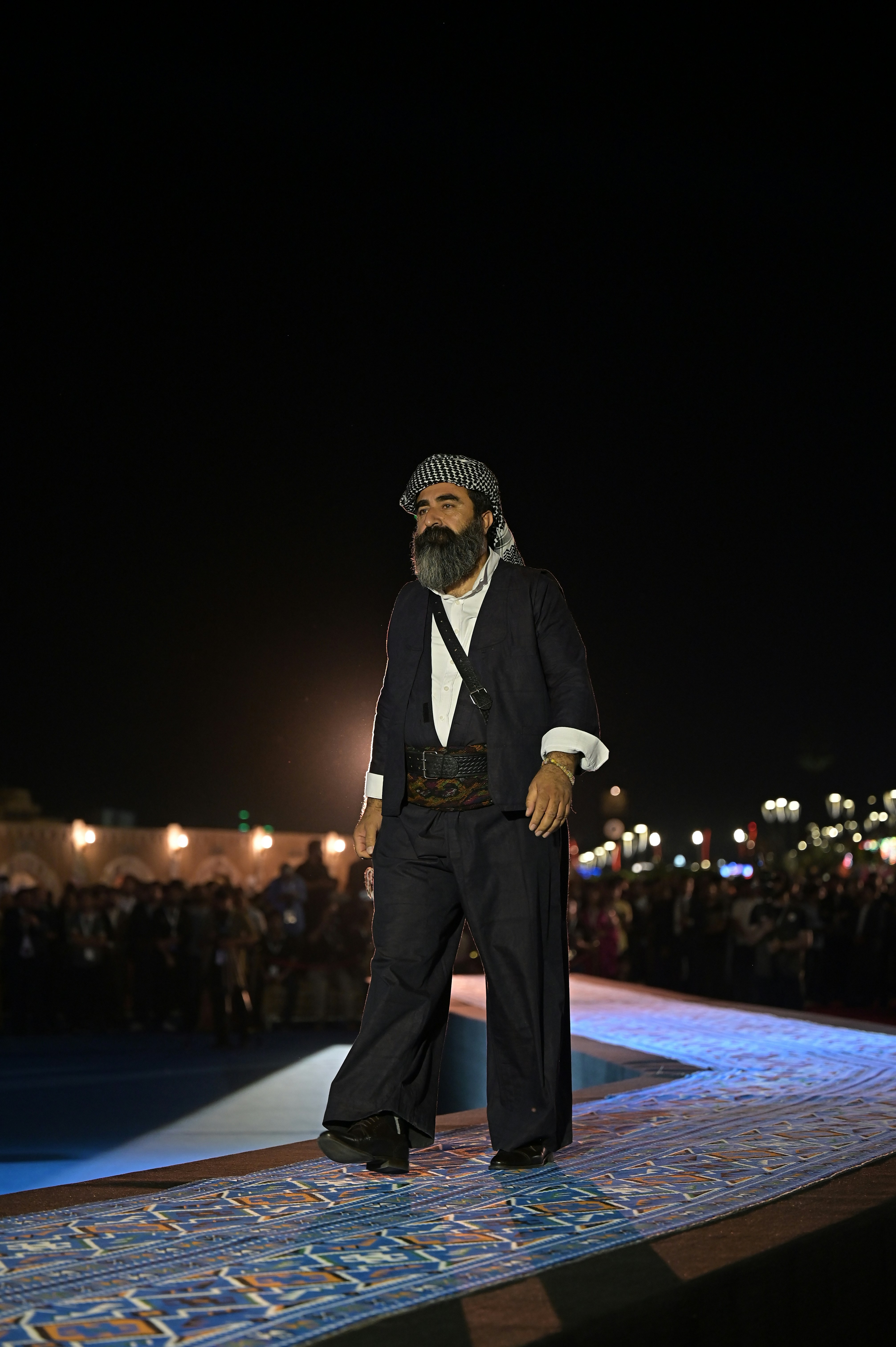 Nocturnal Catwalk: A Dignified Figure in Traditional Attire Steps Along a Lit Runway