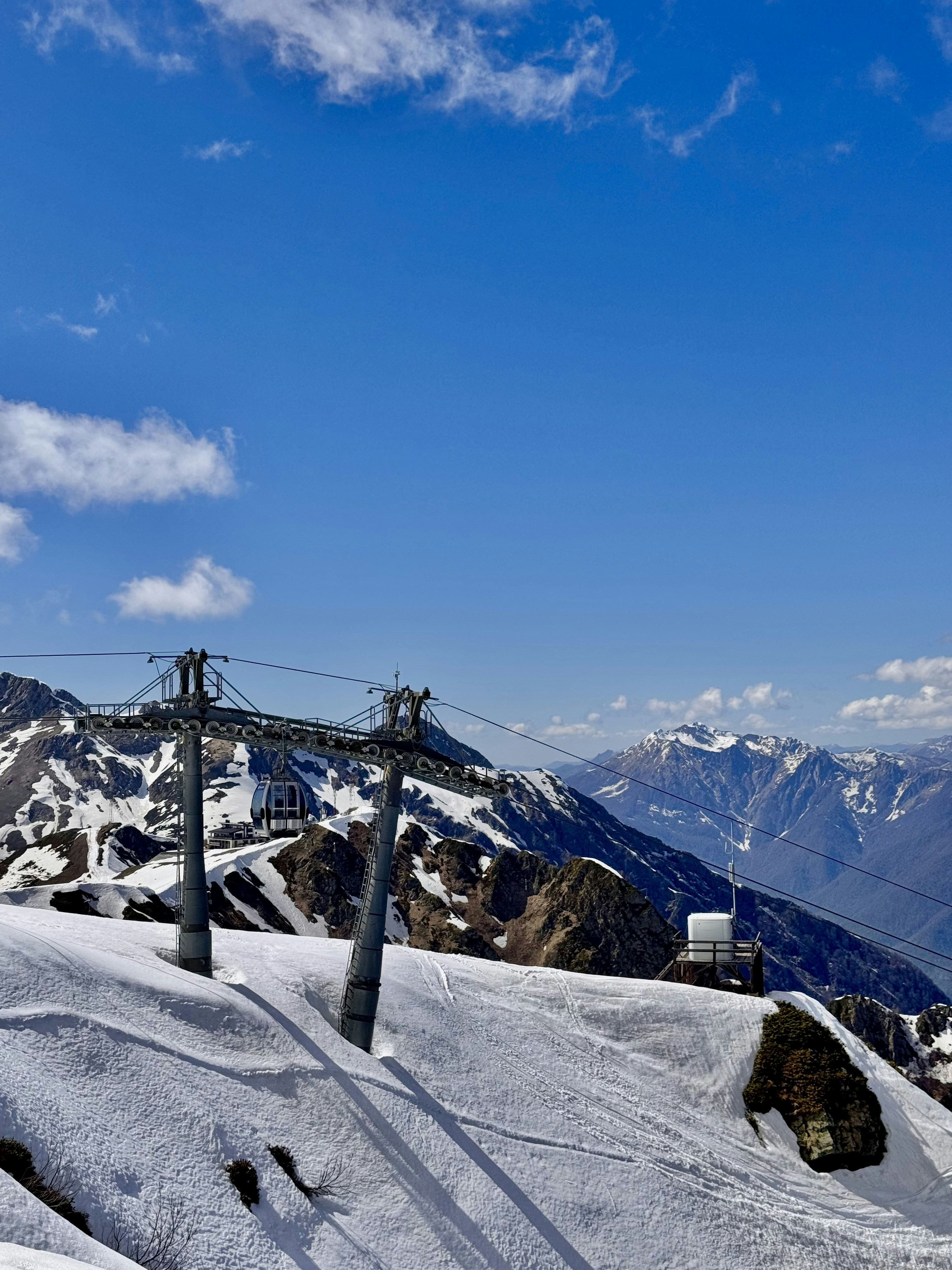 Ski lift atop snow-covered mountain peaks on a bright day.