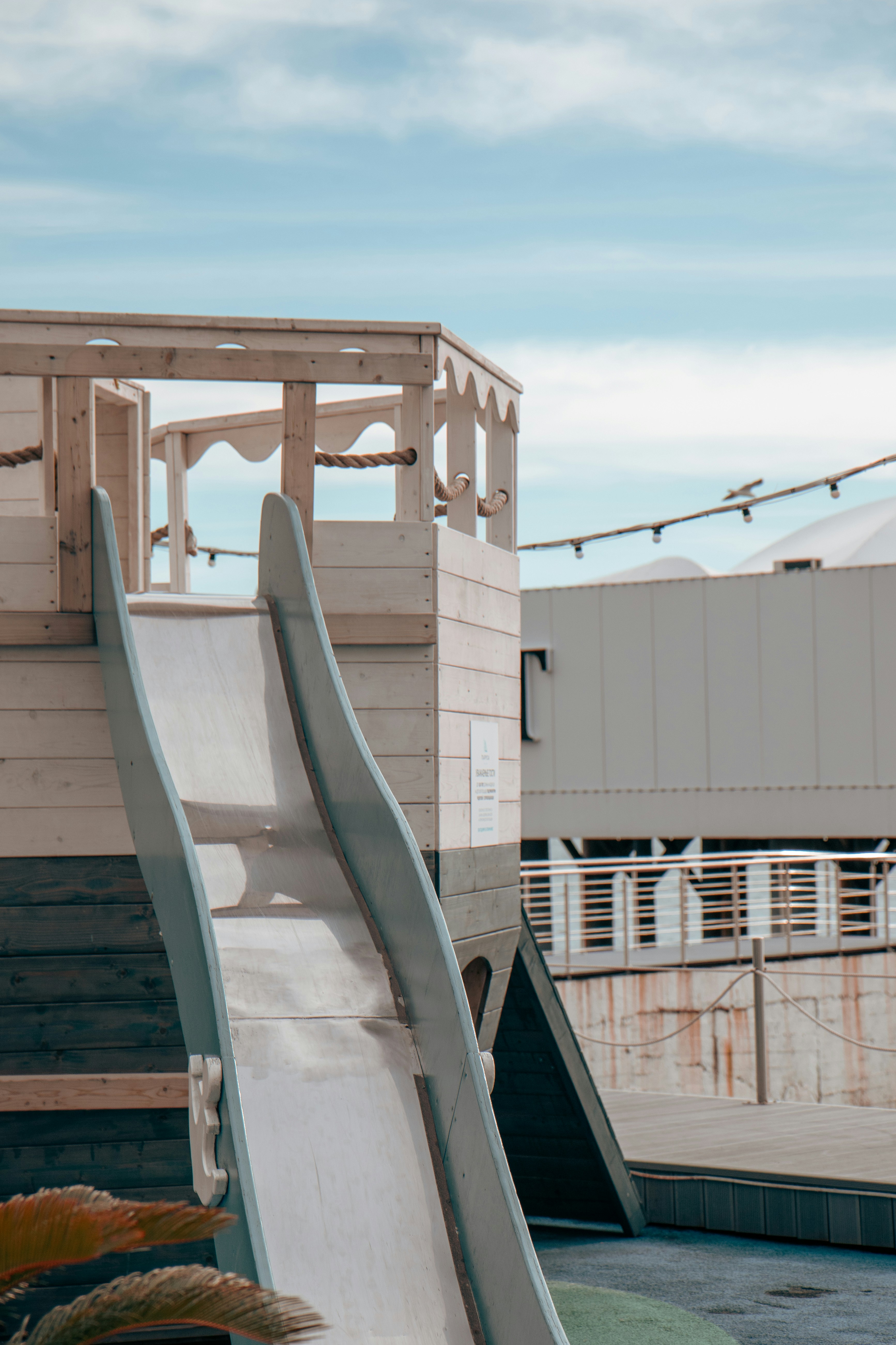 Slide tower over the boardwalk: a sunlit playground structure against a coastal backdrop
