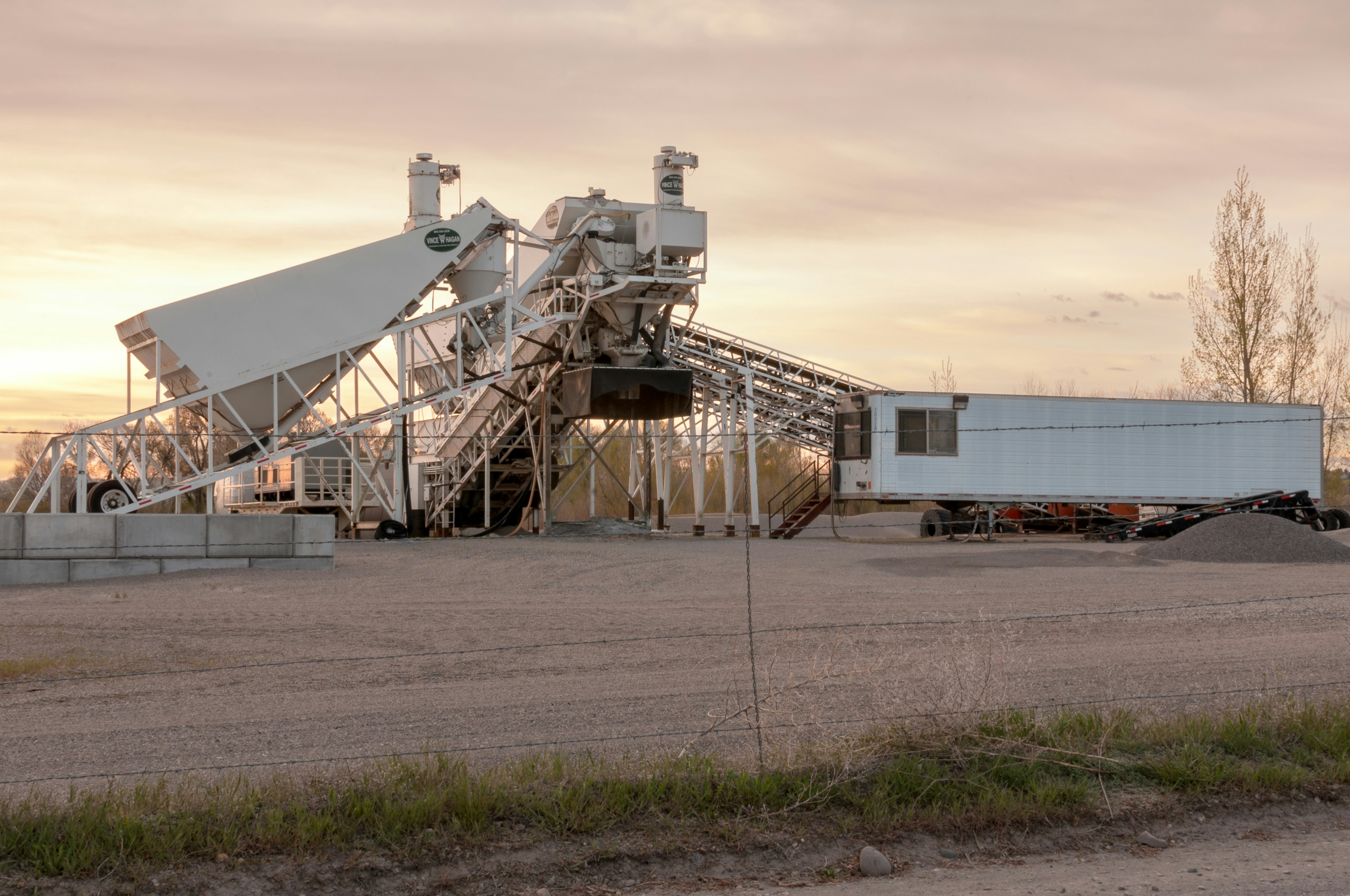 Concrete mixing plant with conveyor systems illuminated by the soft glow of sunset.