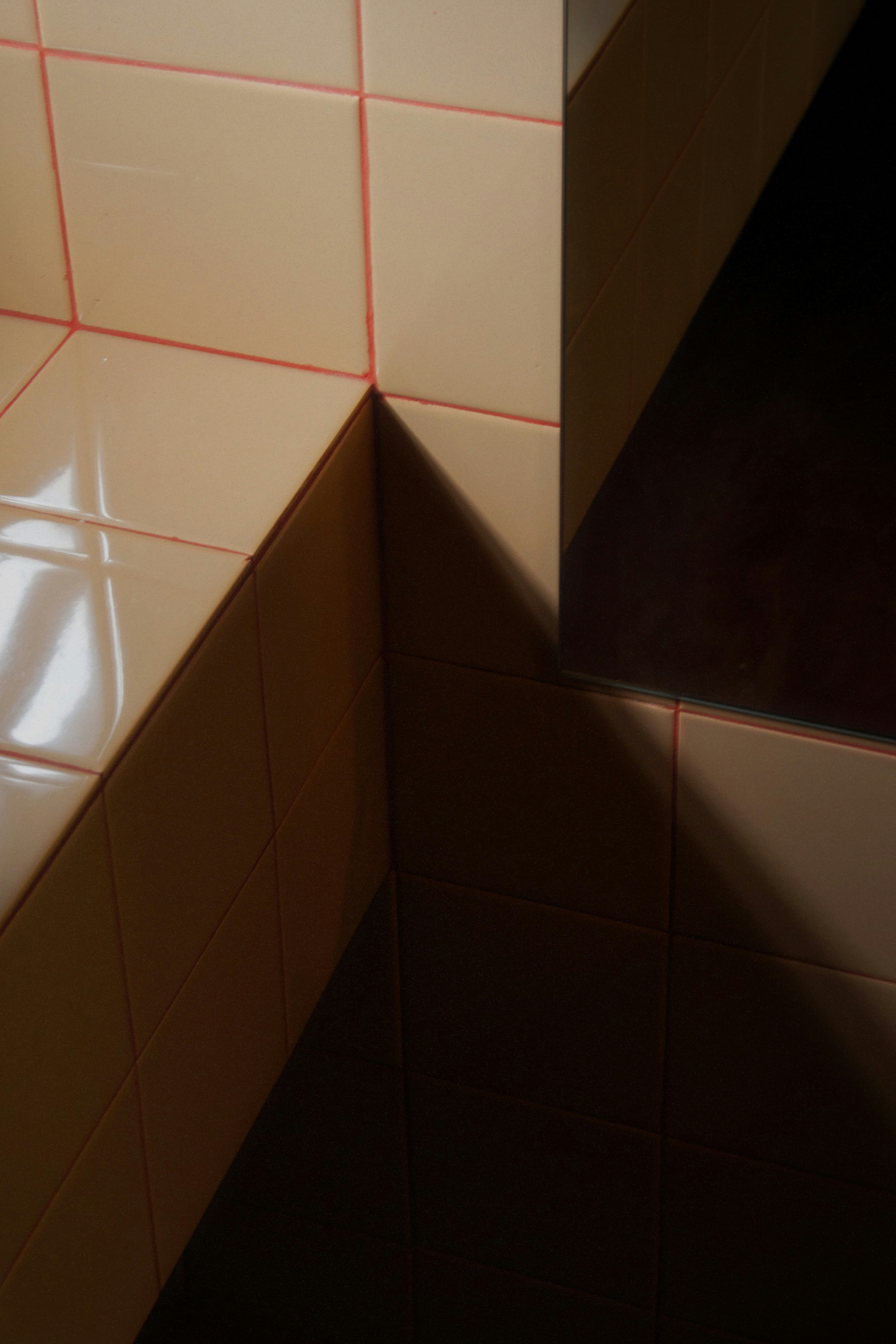 Close-up of glossy tiles intersecting at a corner, with a subtle reflection in the adjacent surface. The interplay of light and shadow creates an intriguing visual texture.