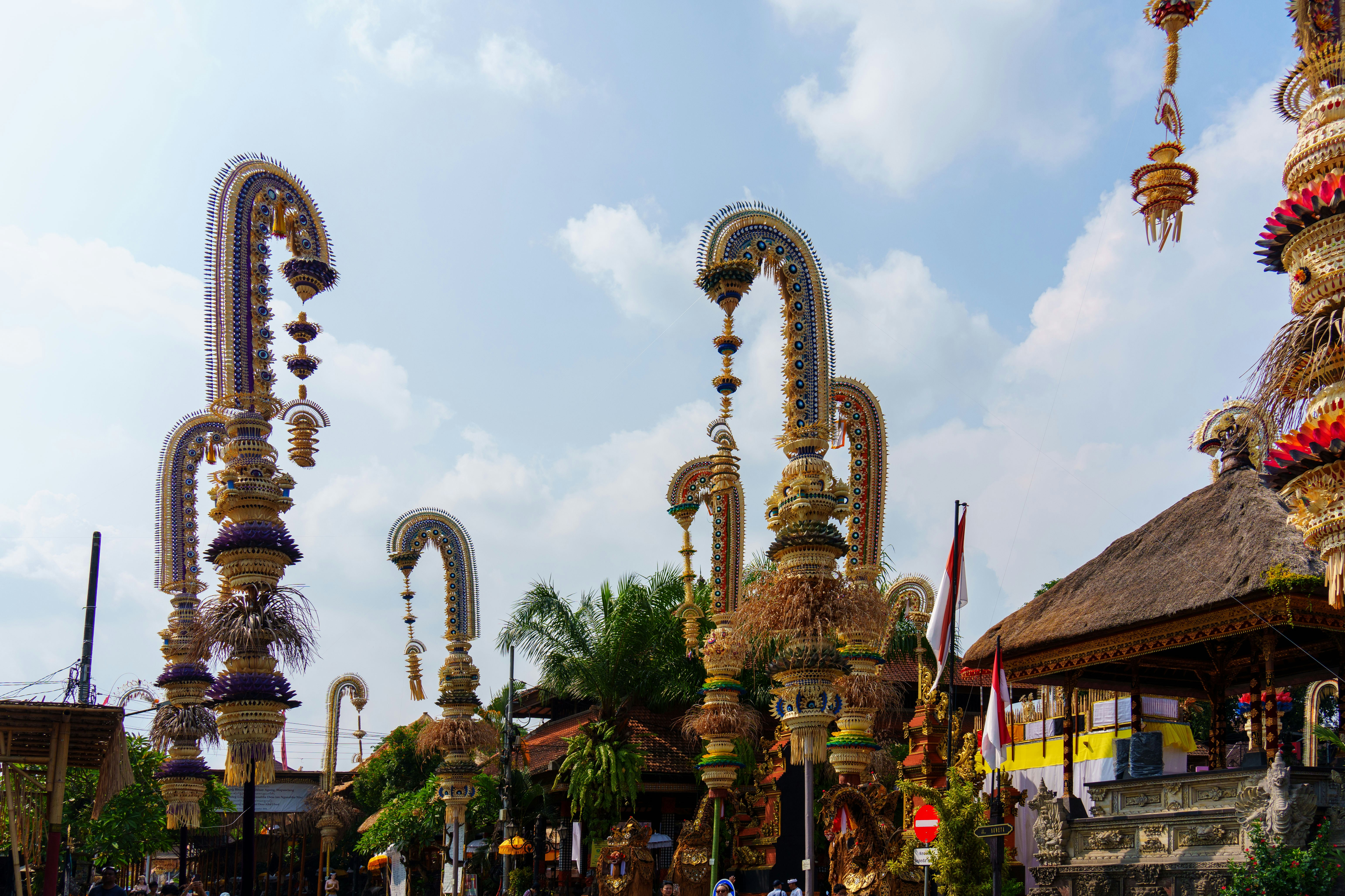 Traditional Balinese penjors adorned with intricate decorations stand tall against a bright blue sky, showcasing cultural significance and artistry.