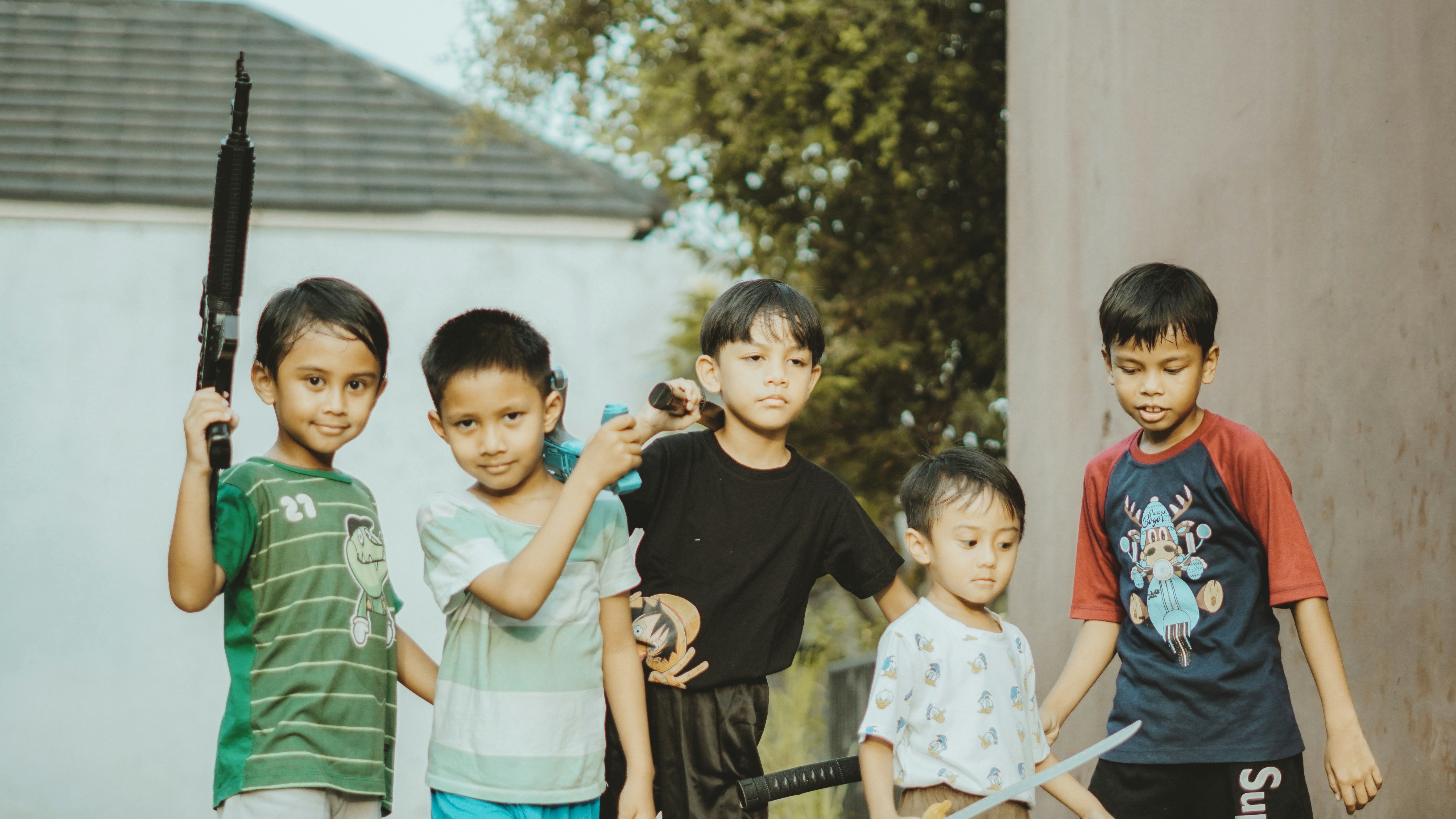 Group of five children posing playfully with toy weapons in an outdoor setting, showcasing their imaginative play.