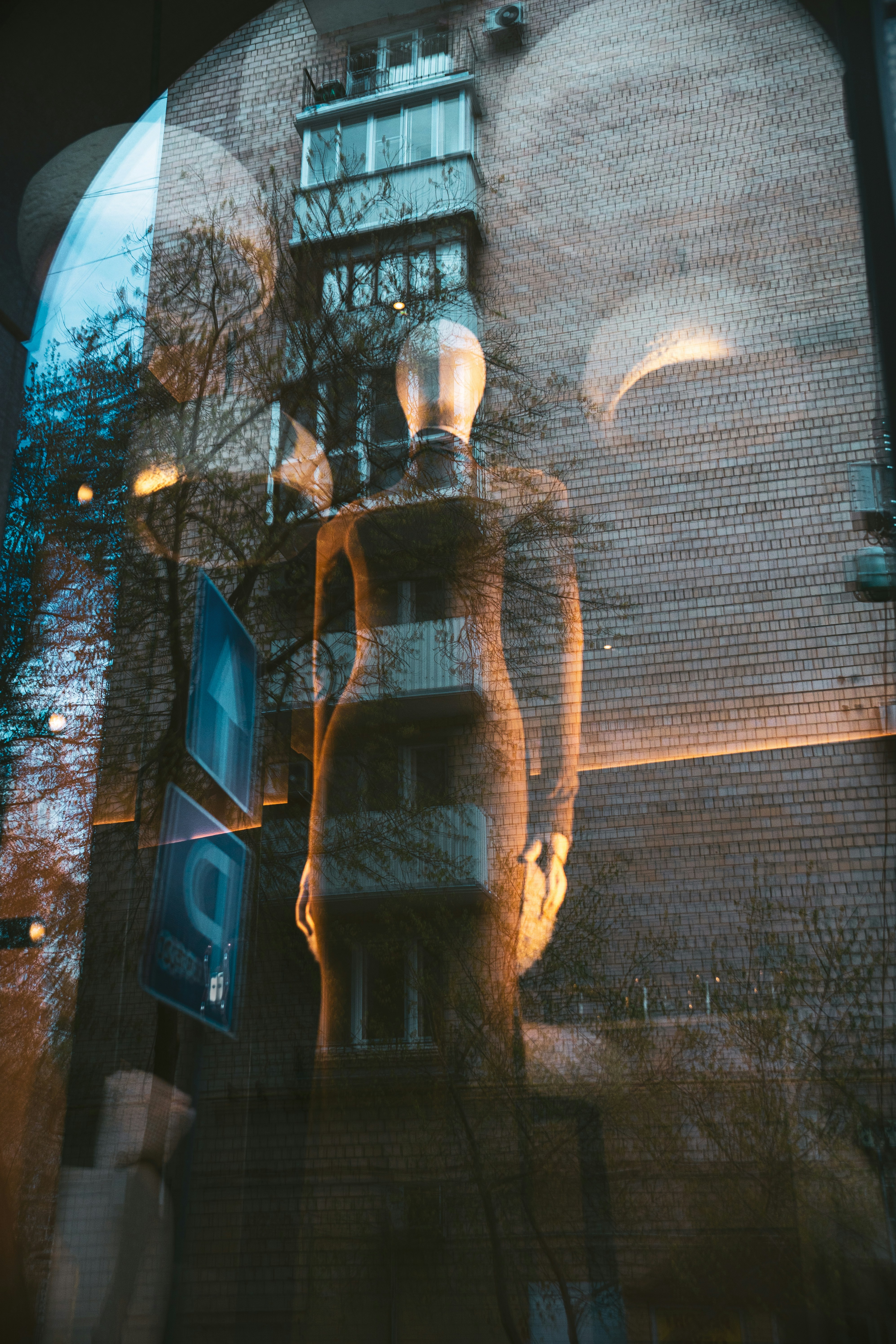 A mannequin in a brown dress is visible through the glass of a boutique’s facade, which reflects a tall urban building.