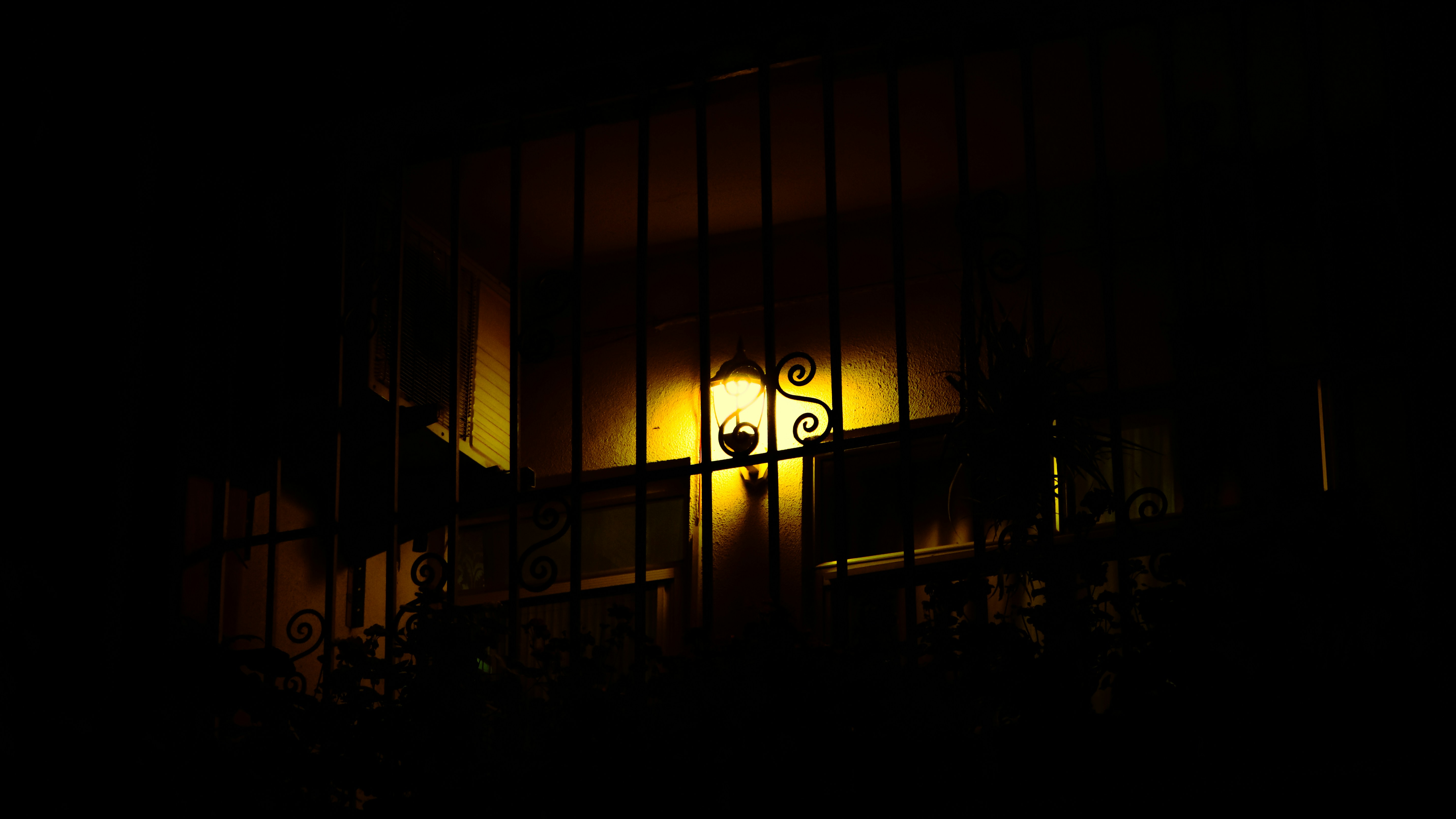 A warm light glows from a window, partially obscured by decorative bars, creating a sense of mystery and intrigue.