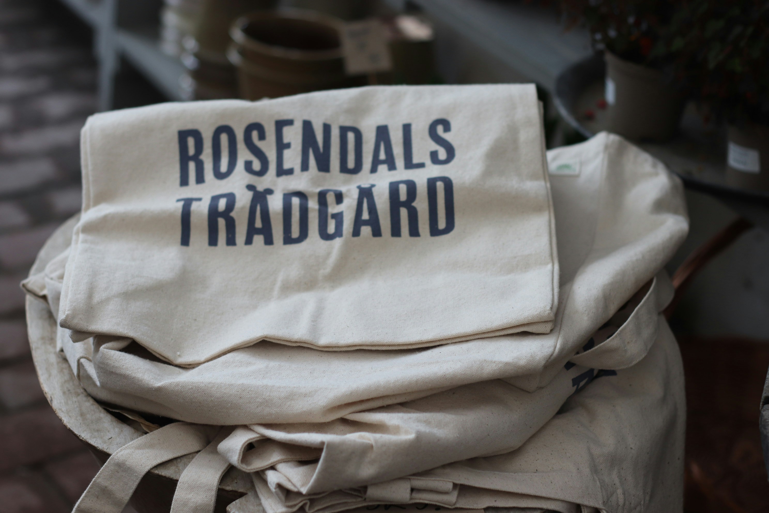 Canvas Tote with Rosendals Trädgård Branding resting on a stack of bags