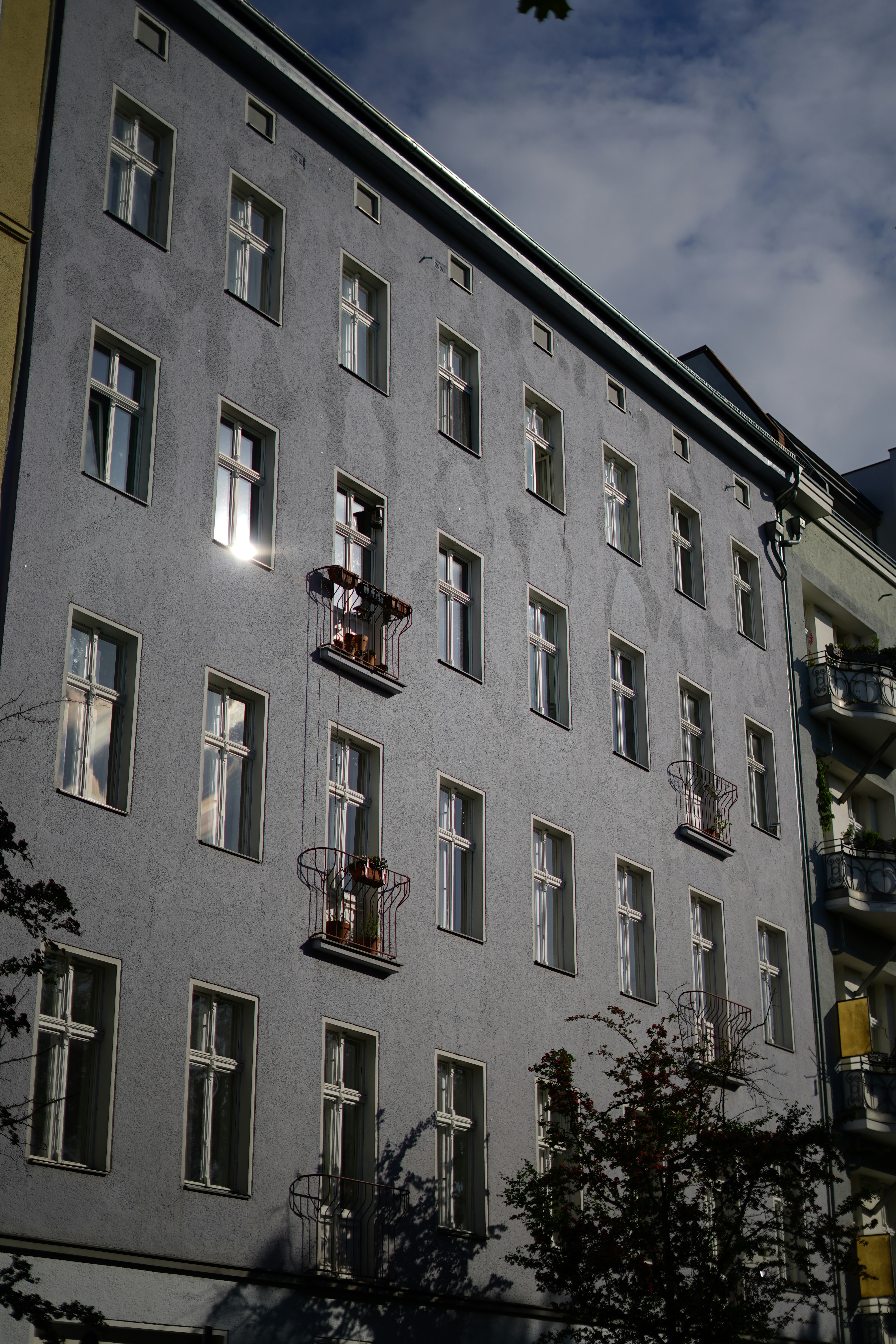Sunlit Glint on a Grey Facade: Reflections Across a Multistory Apartment Wall