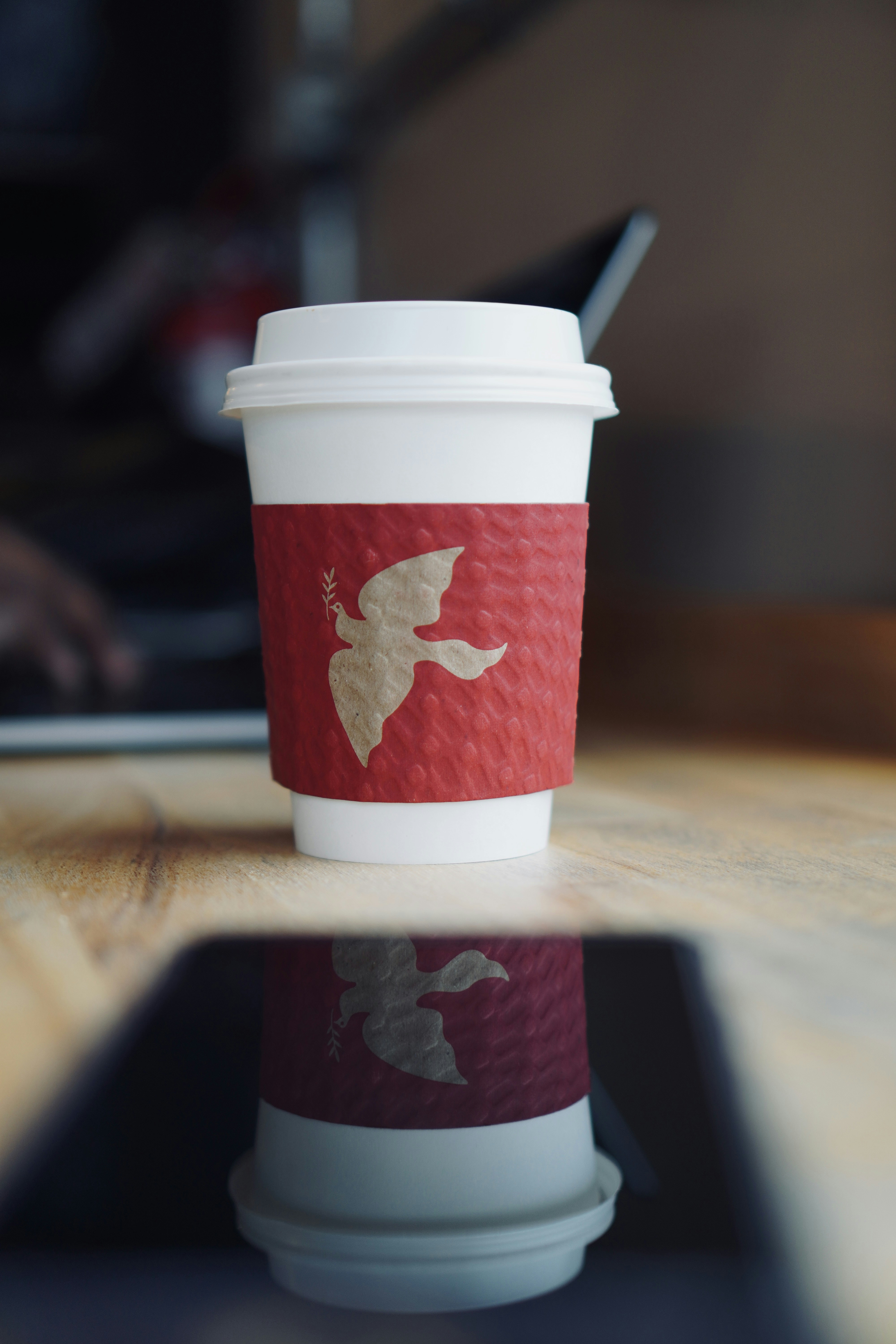 Red-Sleeved Coffee Cup Anchoring a Quiet Moment on a Wooden Counter