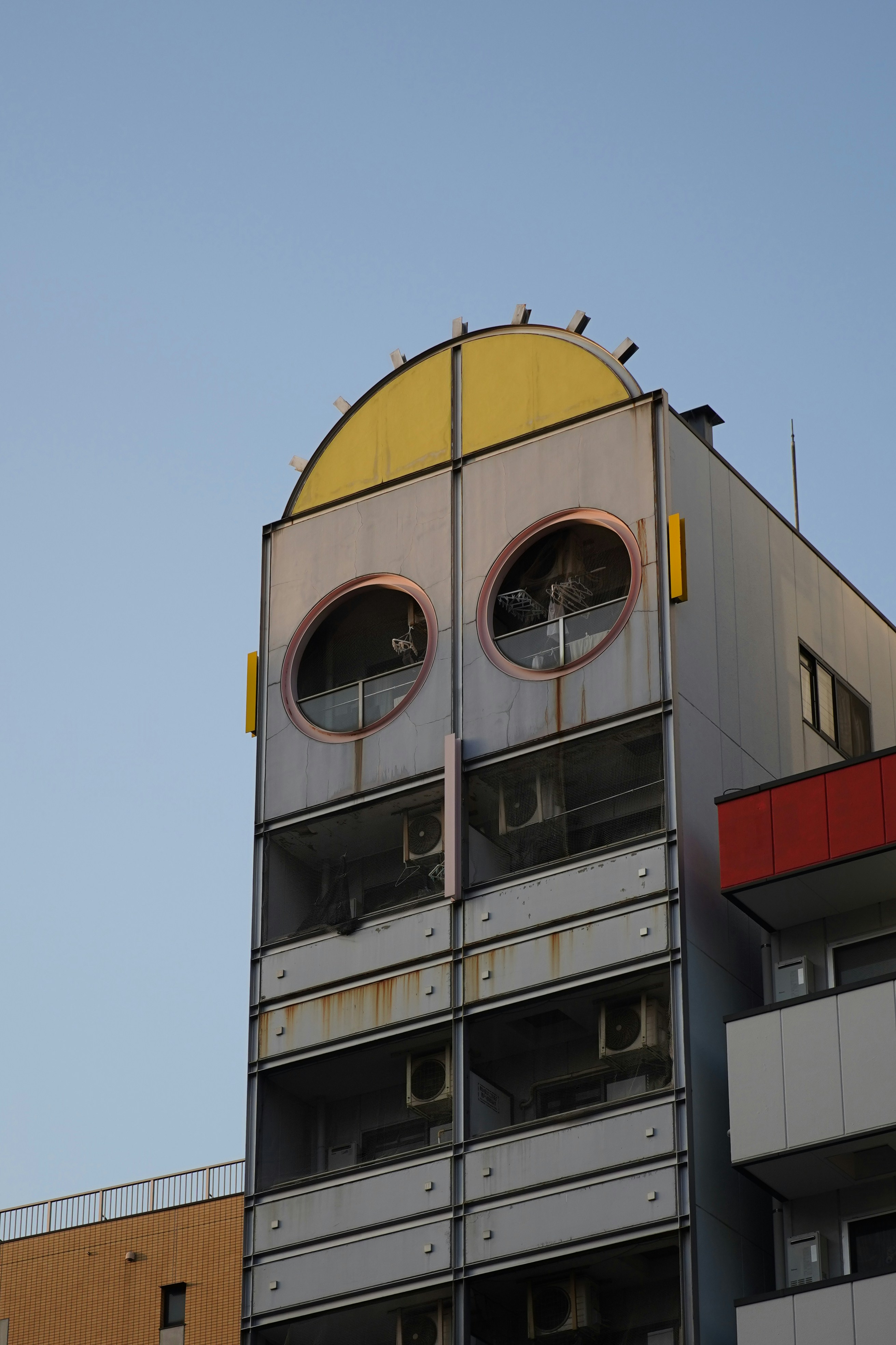 Pink-Rimmed Circles on a Rusted Facade Beneath a Calm Blue Sky