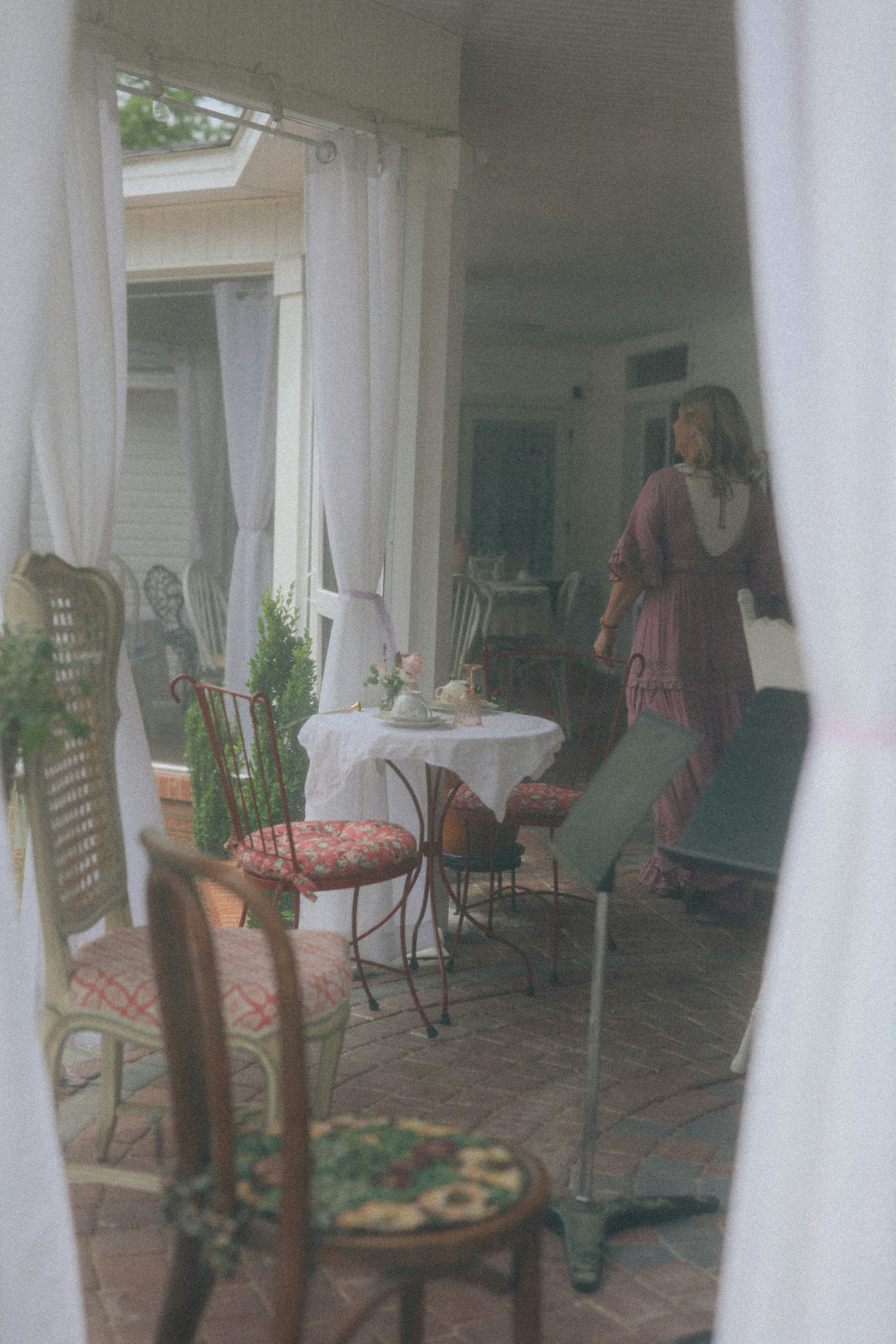 Porch Portrait by White Drapes: A Woman in Burgundy at a Café Table