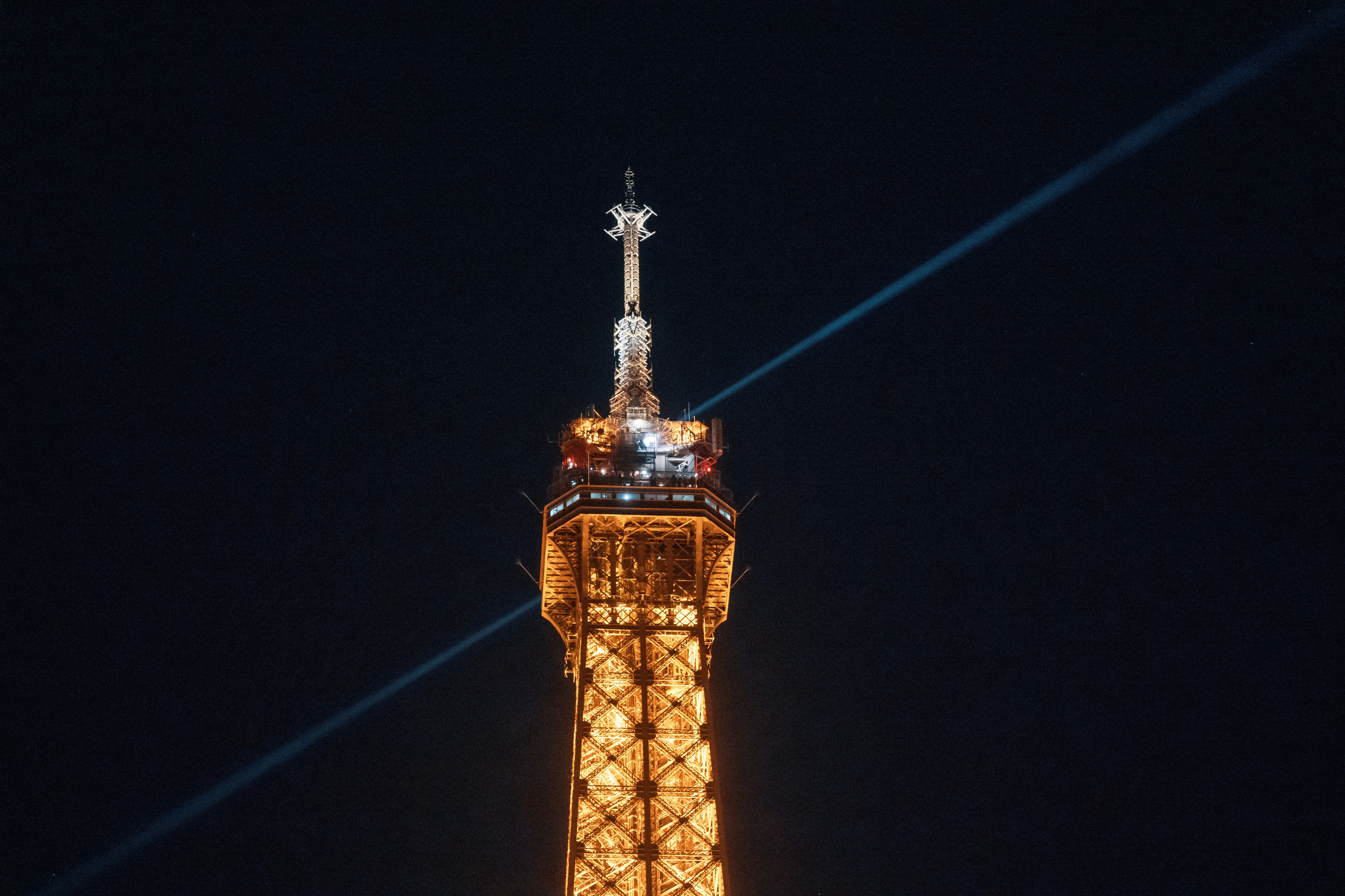 Eiffel tower's illuminated top shines brightly at night.