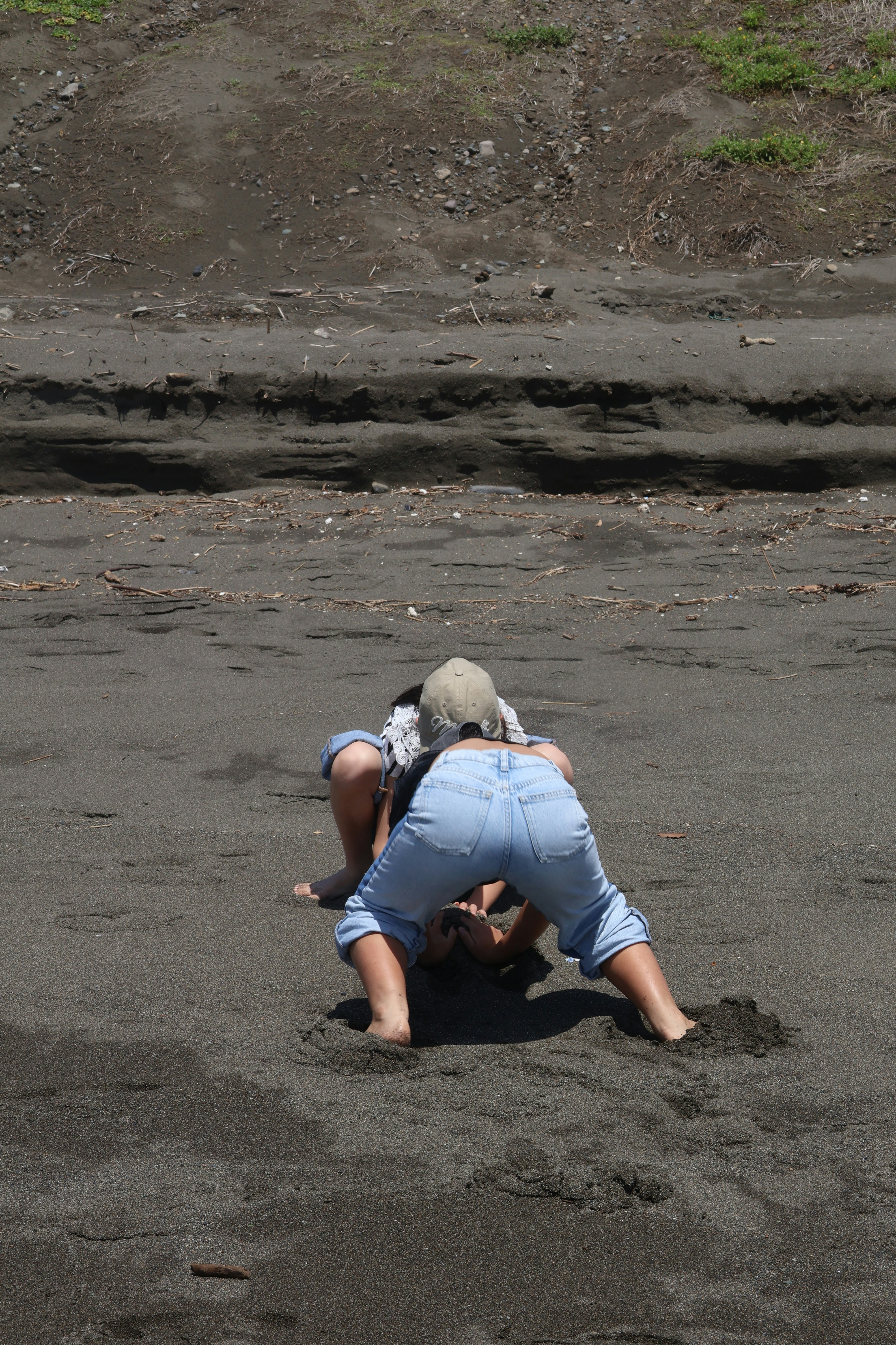 Bottom-leaning peek: child at the riverbank deciphering the sand