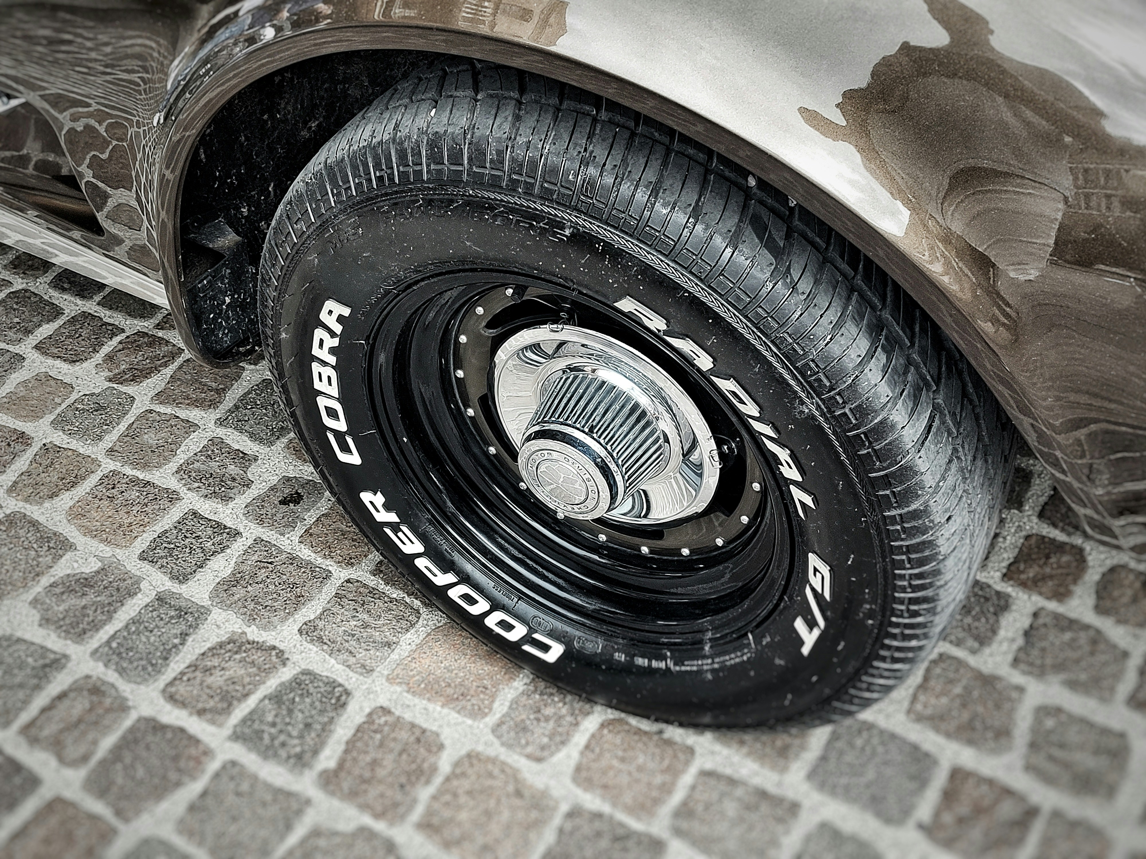 A classic car tire sits on cobblestone pavement.