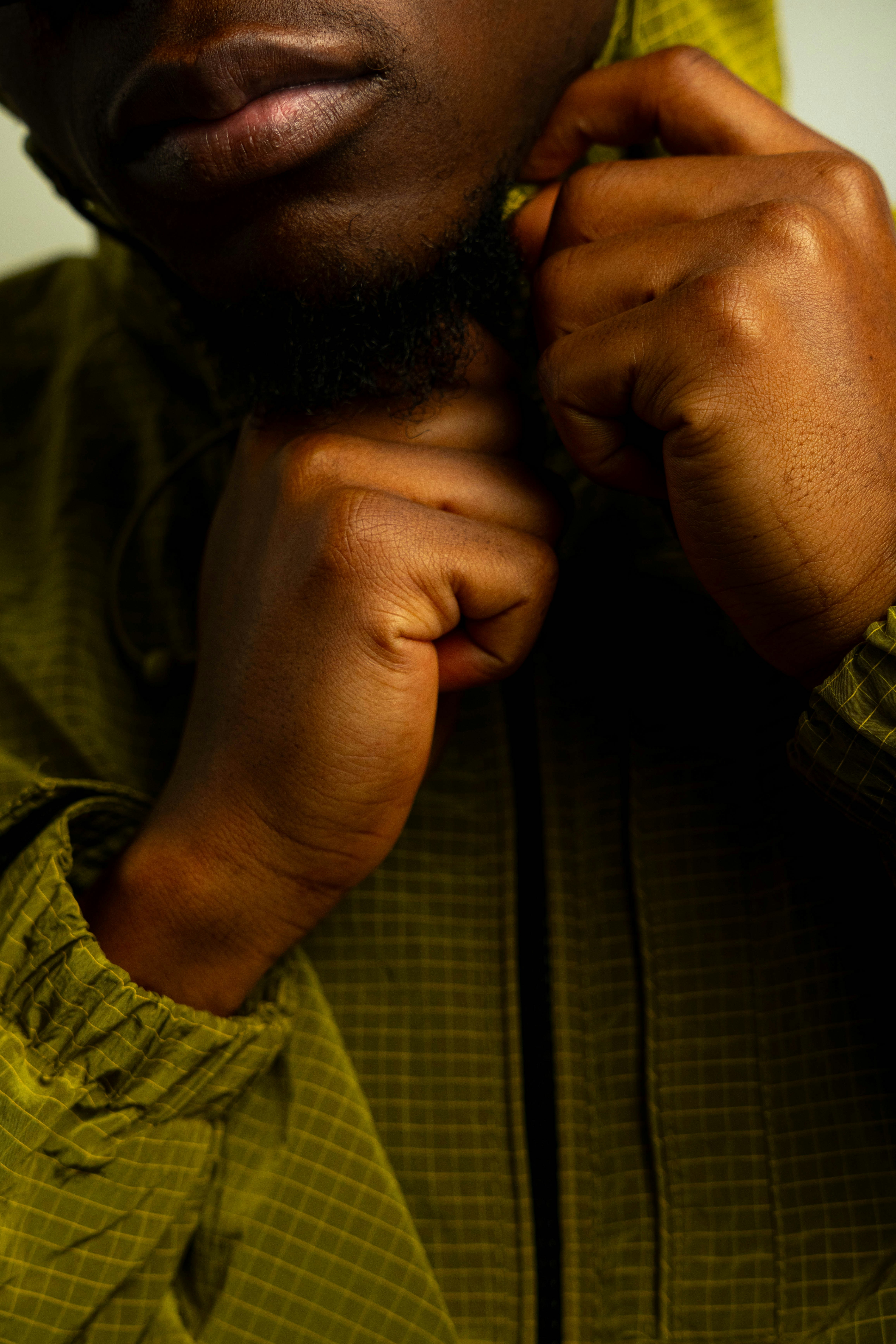 Close-up of a person adjusting their jacket in a contemplative pose, highlighting the texture of the fabric and the intensity of their expression.