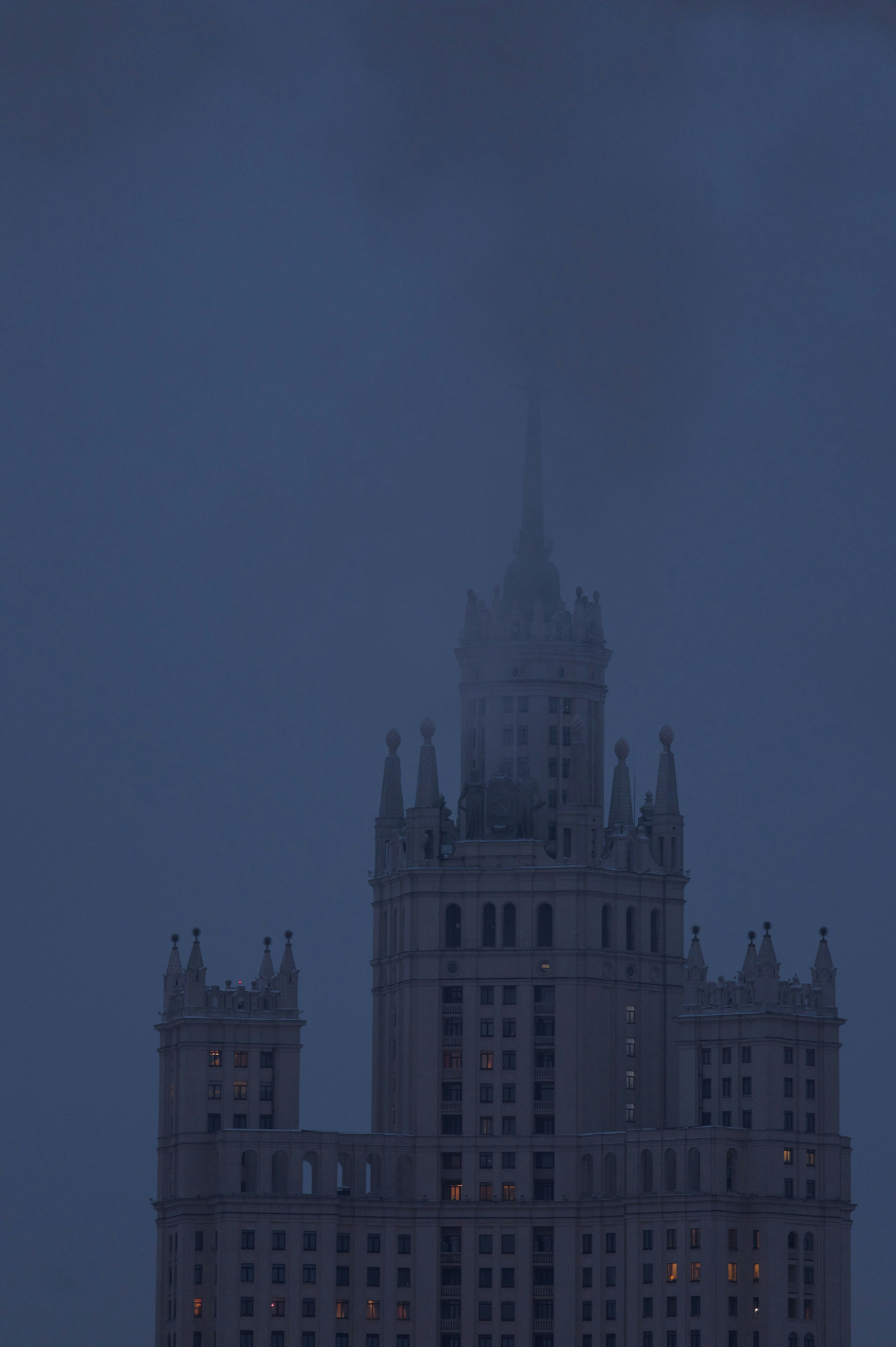 A historic skyscraper emerges through a dense fog, highlighting its intricate architectural details and illuminated windows.