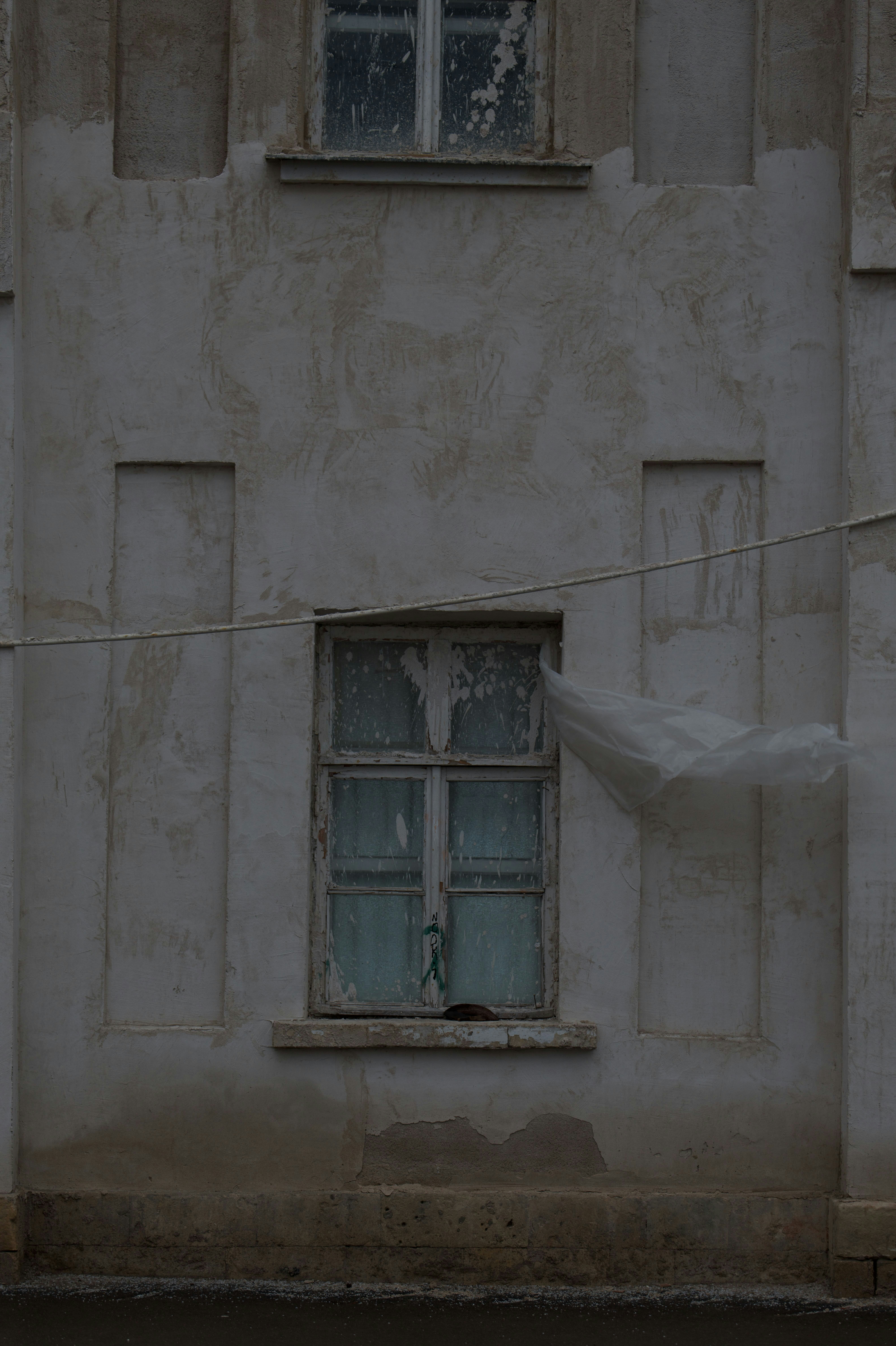 A weathered wall with a solitary window, partially obscured by a sheer fabric, evokes a sense of nostalgia and desolation.