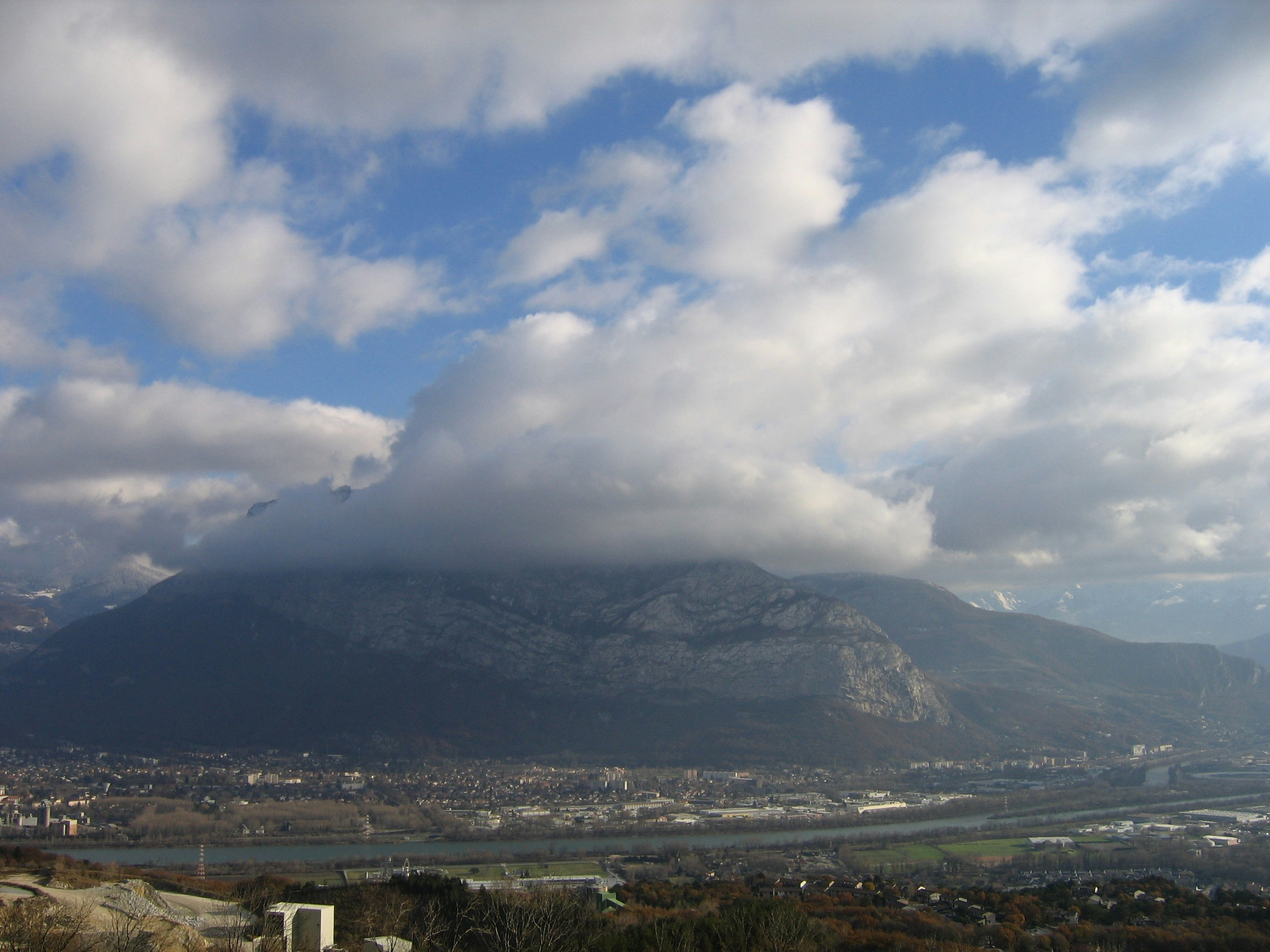 Clouds enveloping a mountain range with a valley below, showcasing the interplay of light and shadow. The scene captures the tranquil beauty of nature.
