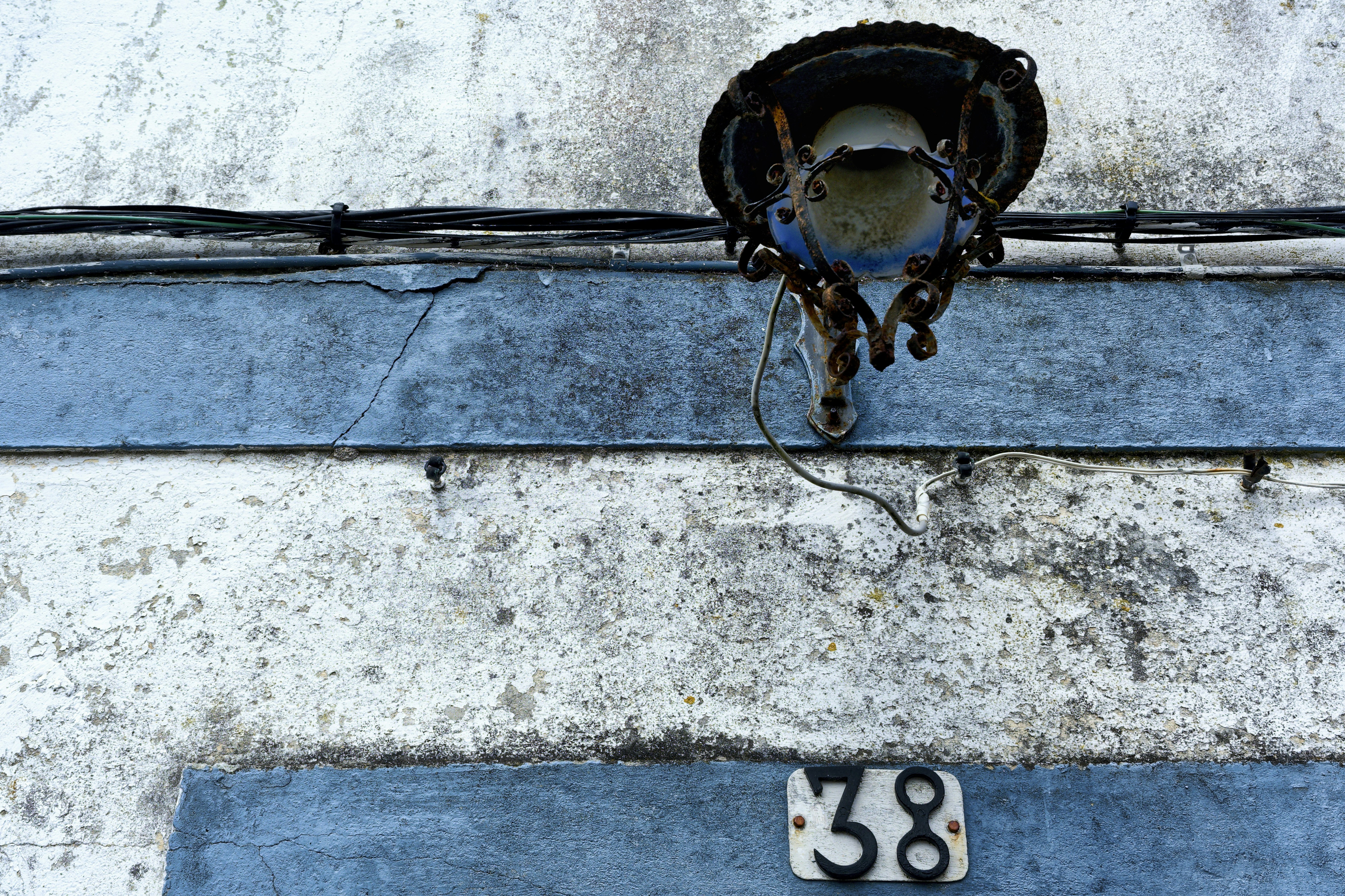 Wall features unique lantern and house number in vibrant blue and white setting - A decorative lantern hangs from a textured wall painted in blue and white. Below, the house number 38 is displayed, adding charm to the exterior.