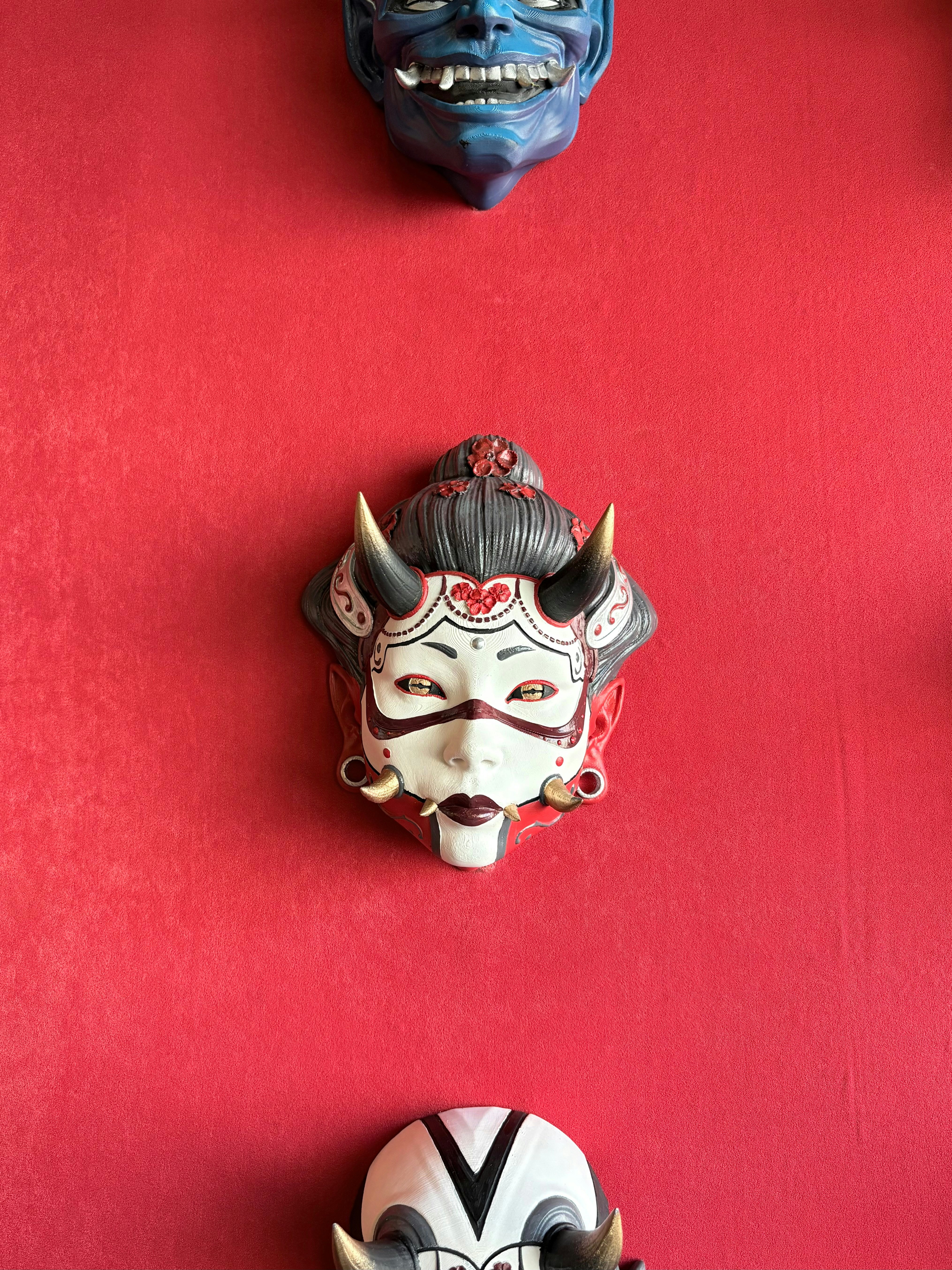 Three japanese masks hang on a red wall.