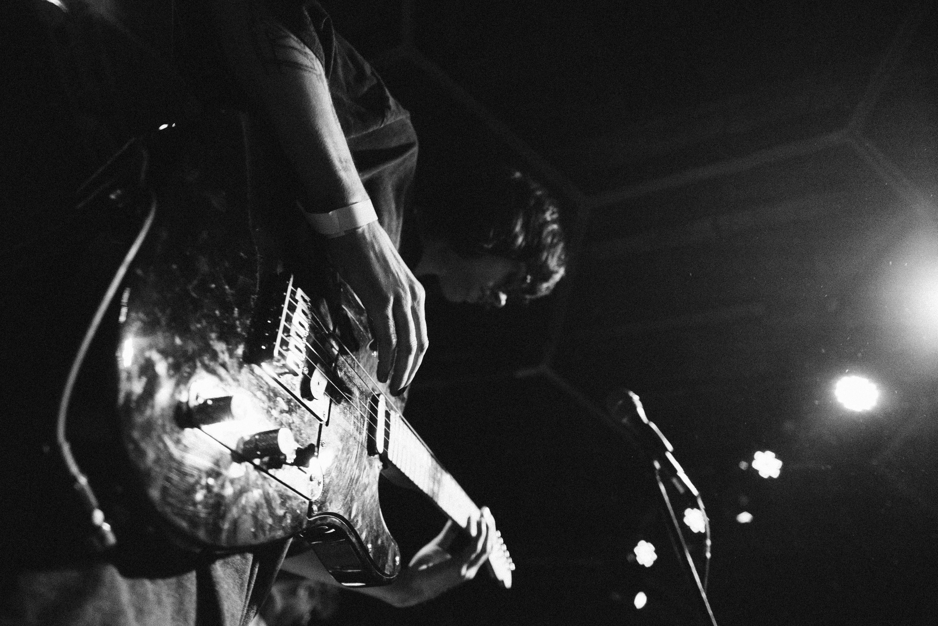 Musician passionately playing an electric guitar under dramatic stage lighting, capturing the essence of live music. Black and white tones enhance the mood.